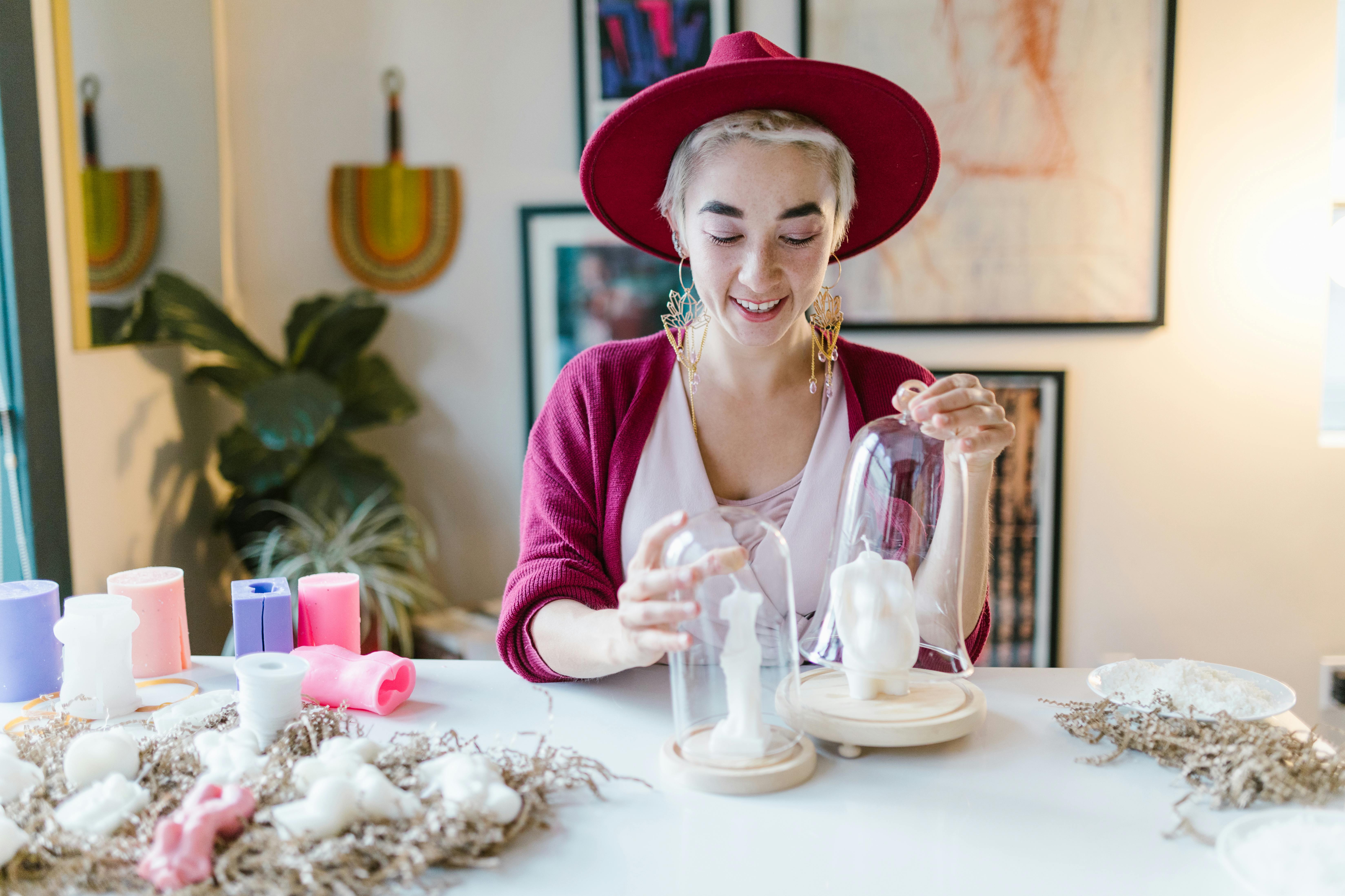 Woman in Red Hat Opening Candles Under Glass Cylinders · Free Stock Photo