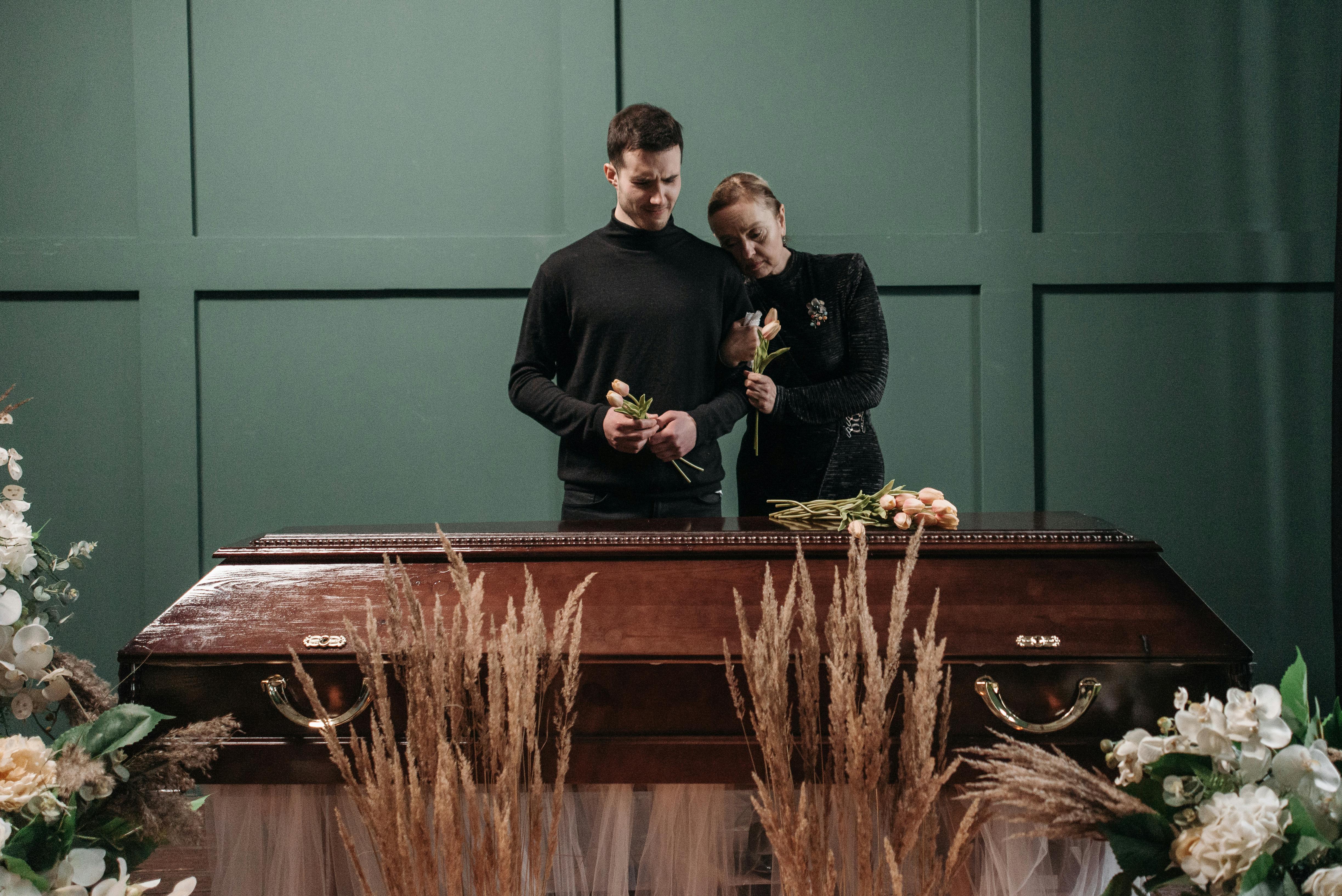 An Elderly Woman Leaning on a Man's Shoulder Near a Wooden Coffin ...