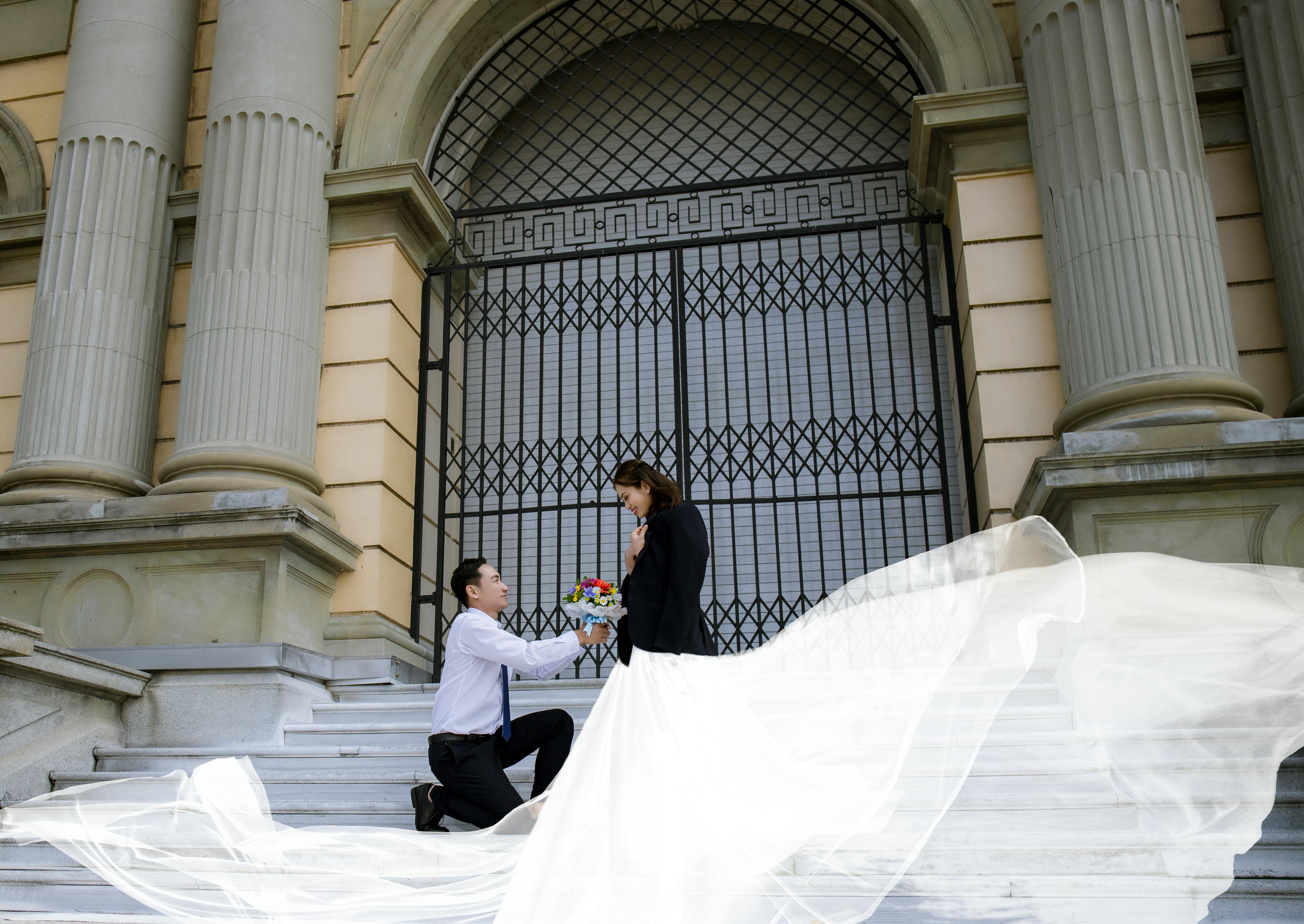 Man Proposing on Stairs with Flowers to Woman in White Dress Flowing in ...