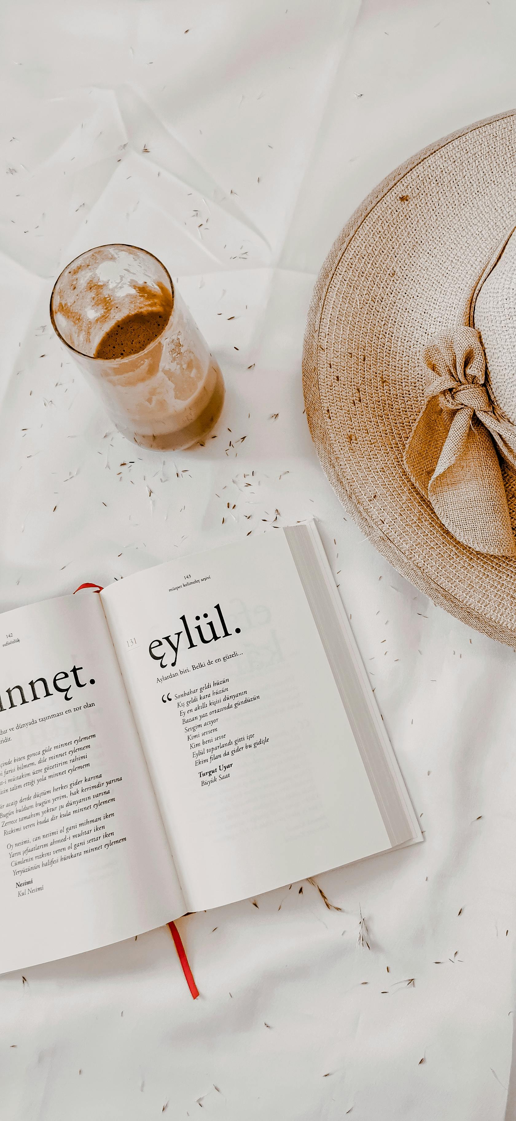 An Open Book beside a Sun Hat and Glass of Drink · Free Stock Photo