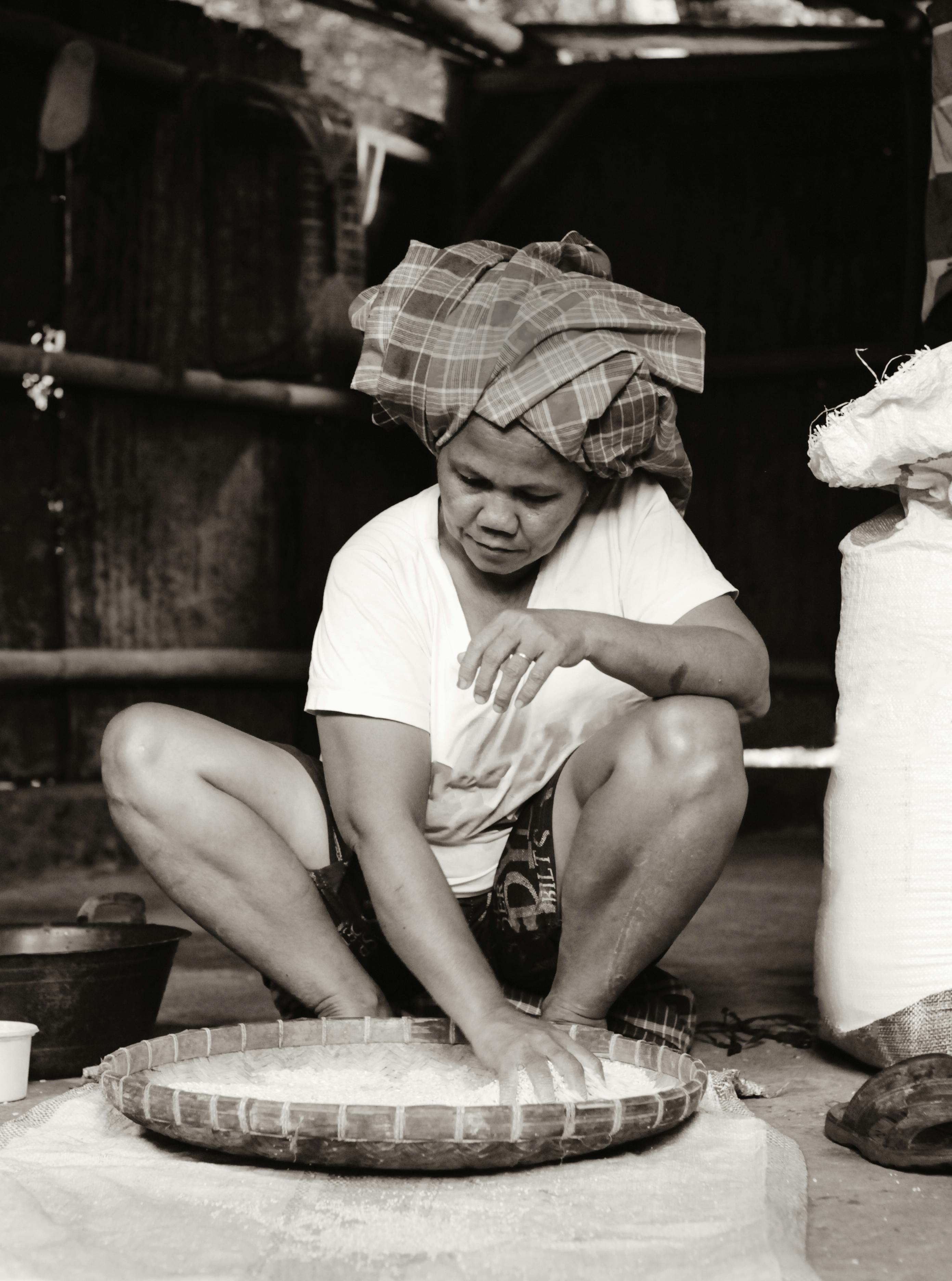 Woman Winnowing Grains while Sitting on the Ground · Free Stock Photo