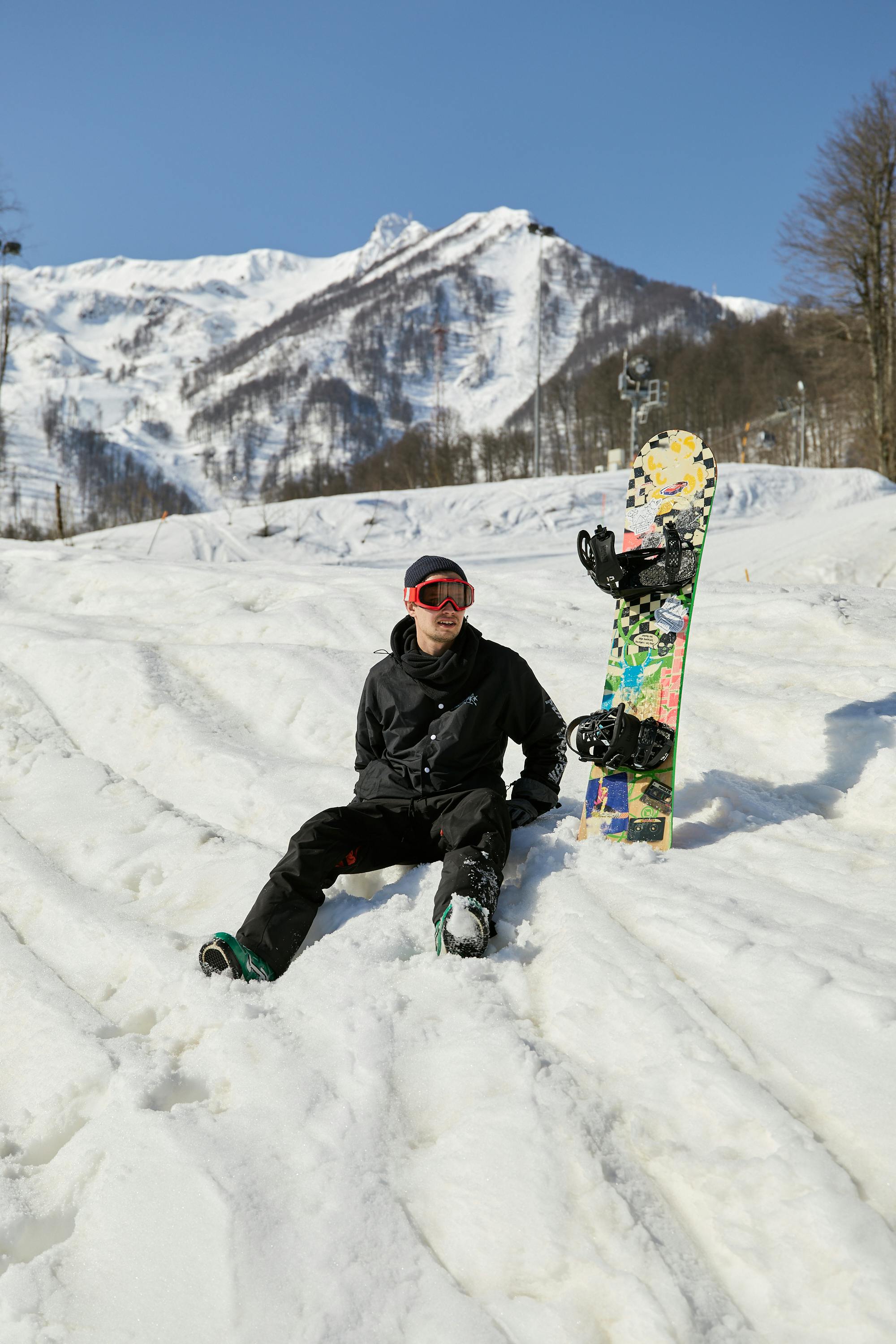 A Man Sitting on the Snow Beside a Snowboard · Free Stock Photo
