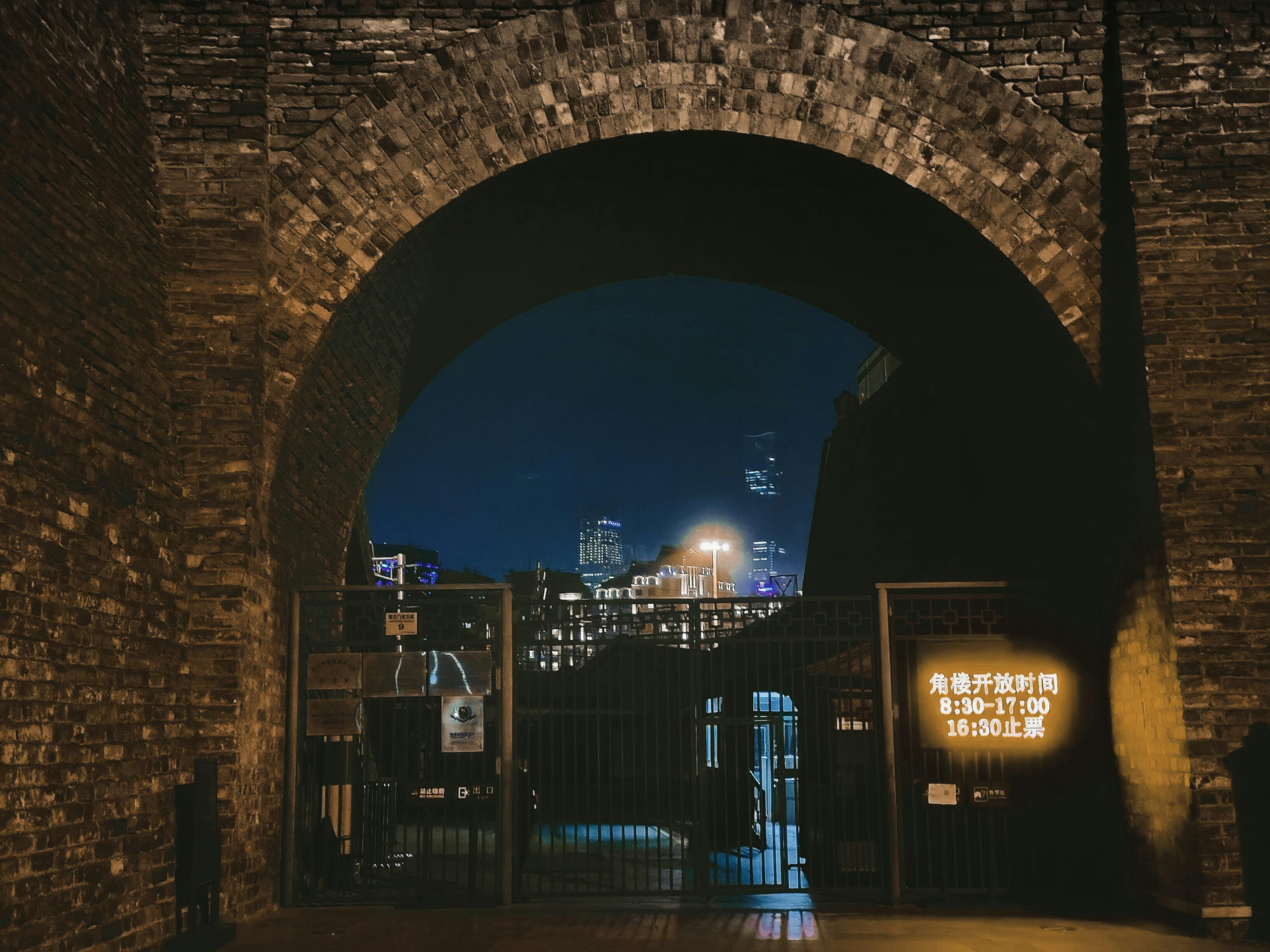 Brick Gate and a Modern City Illuminated at Night · Free Stock Photo