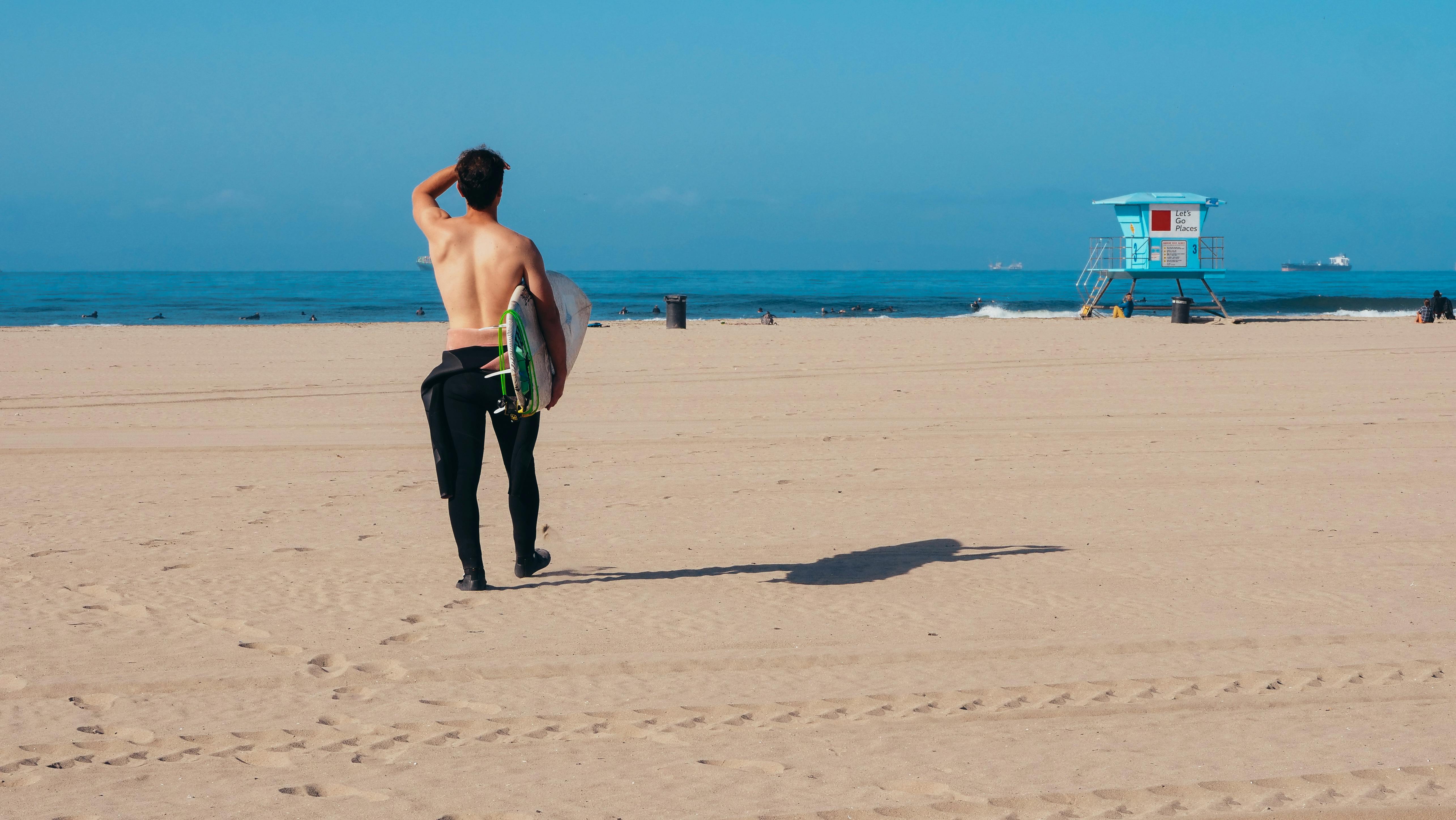A Back View of a Man Walking on the Beach while Carrying His Surfboard ...