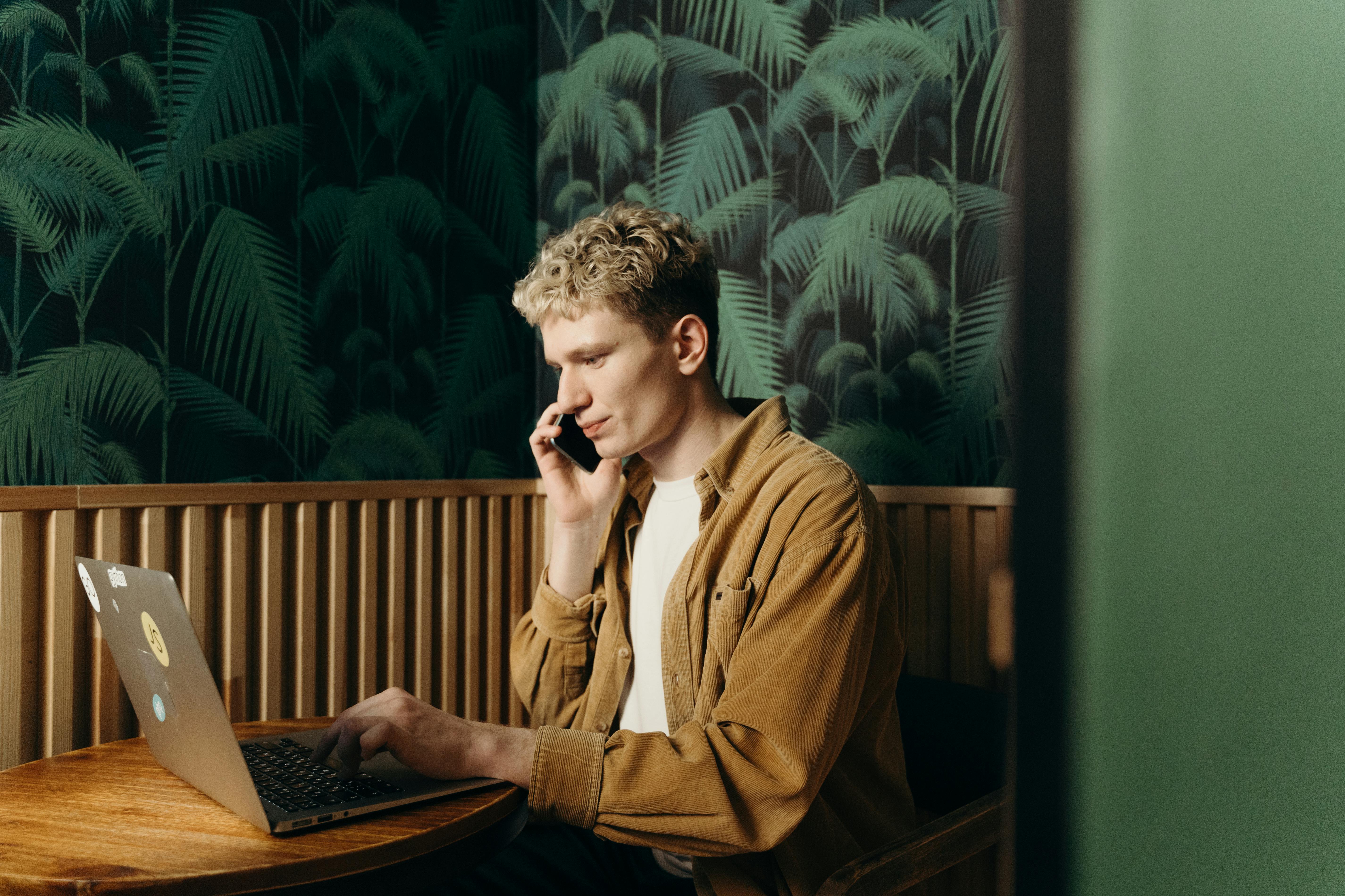 Man in Talking on the Phone While Using a Laptop · Free Stock Photo