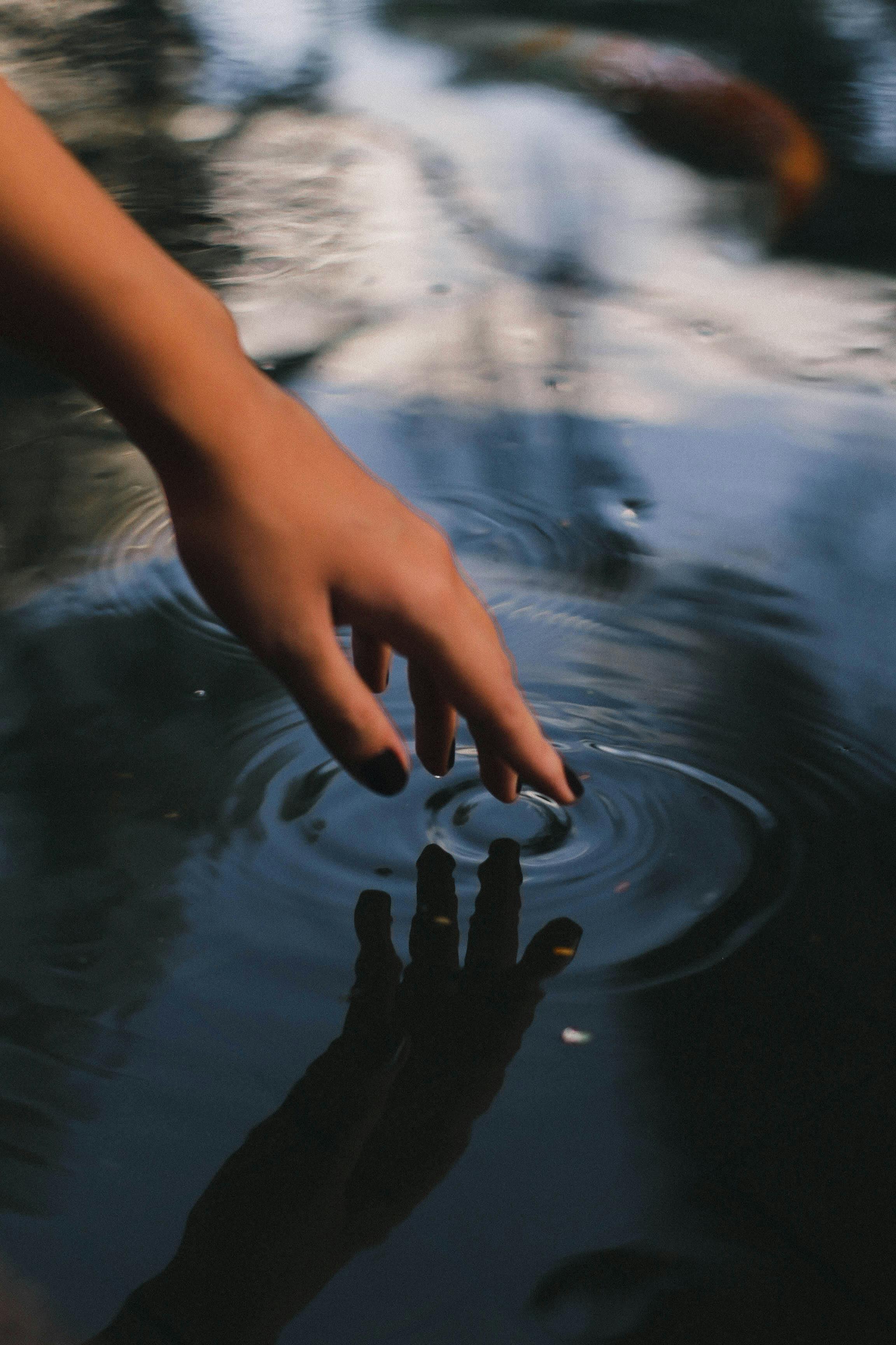 Close-Up Photo of a Person's Hand Touching Body of Water · Free Stock Photo