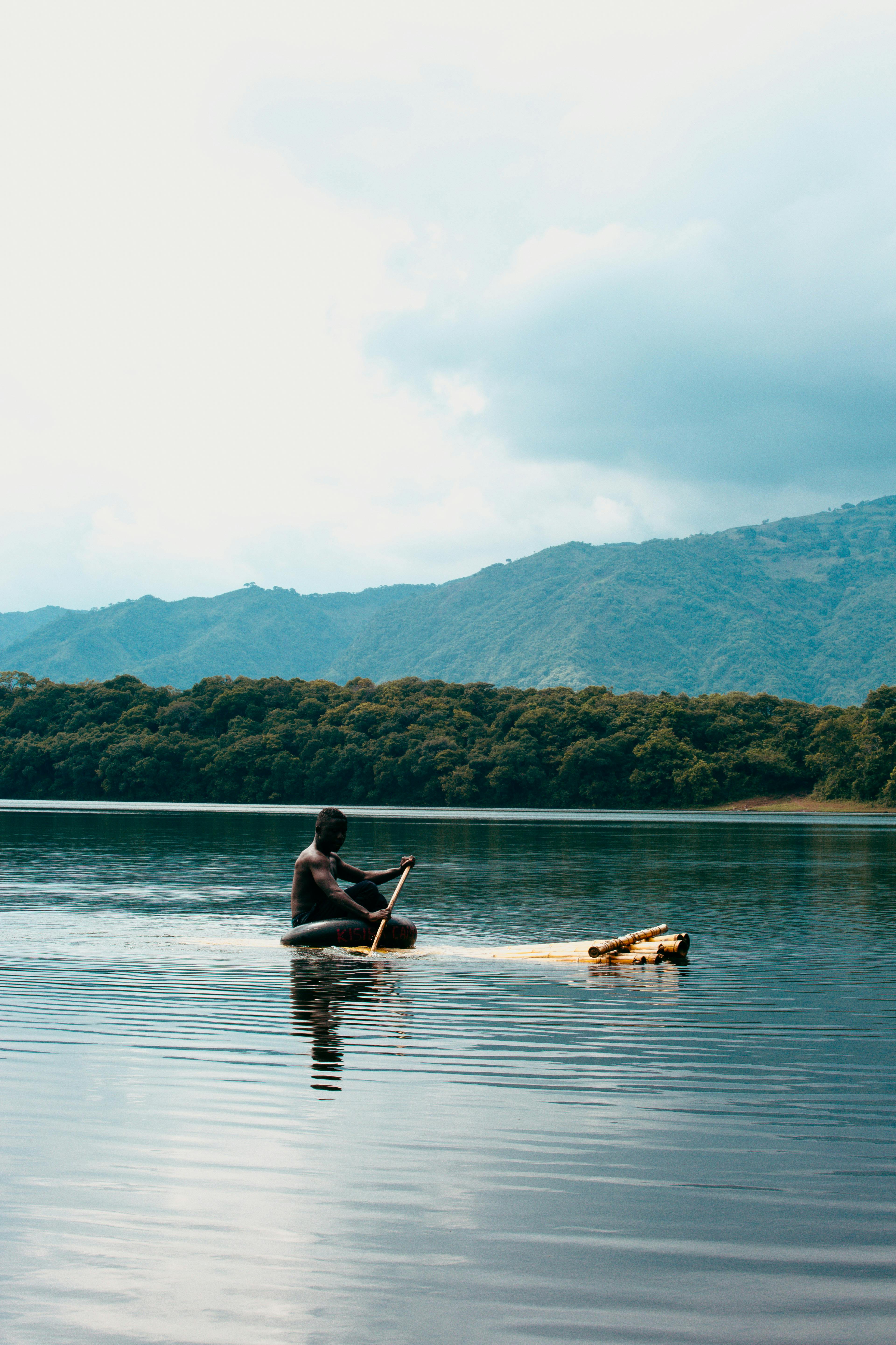 Unrecognizable black man on raft sailing on lake against ridge · Free ...