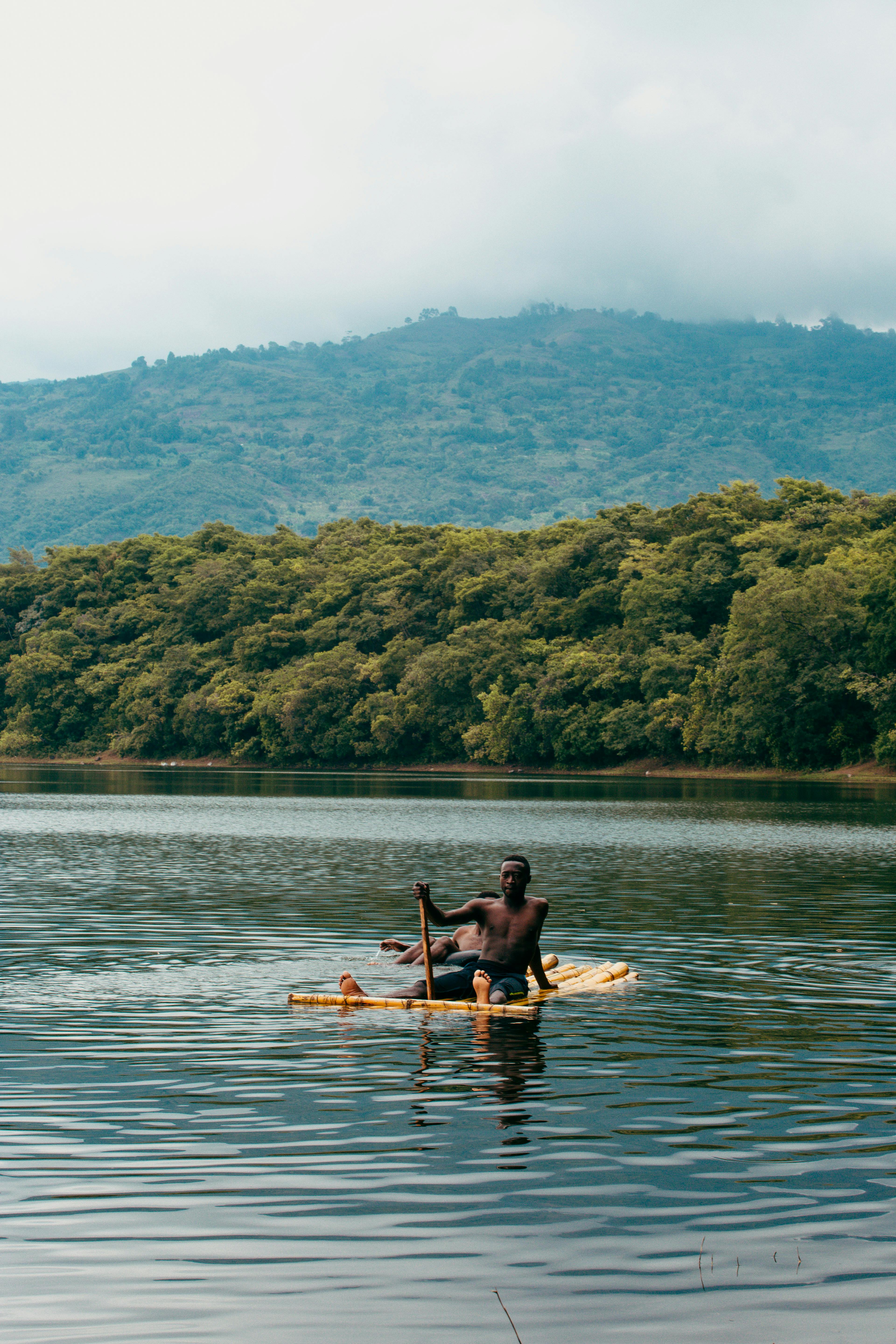 African man on raft on river against trees and mount · Free Stock Photo
