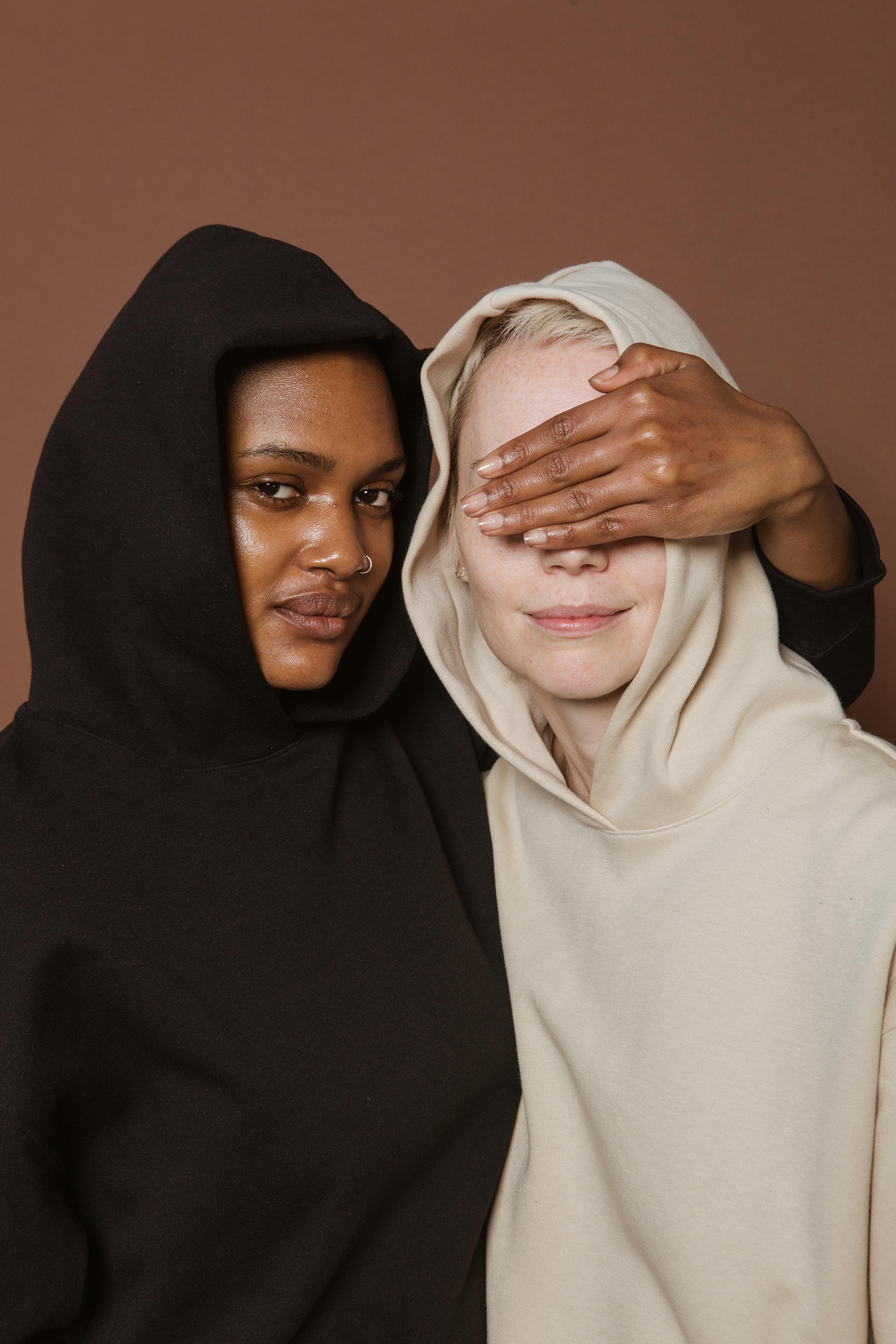 Anonymous black woman covering eyes of female friend in brown studio ...