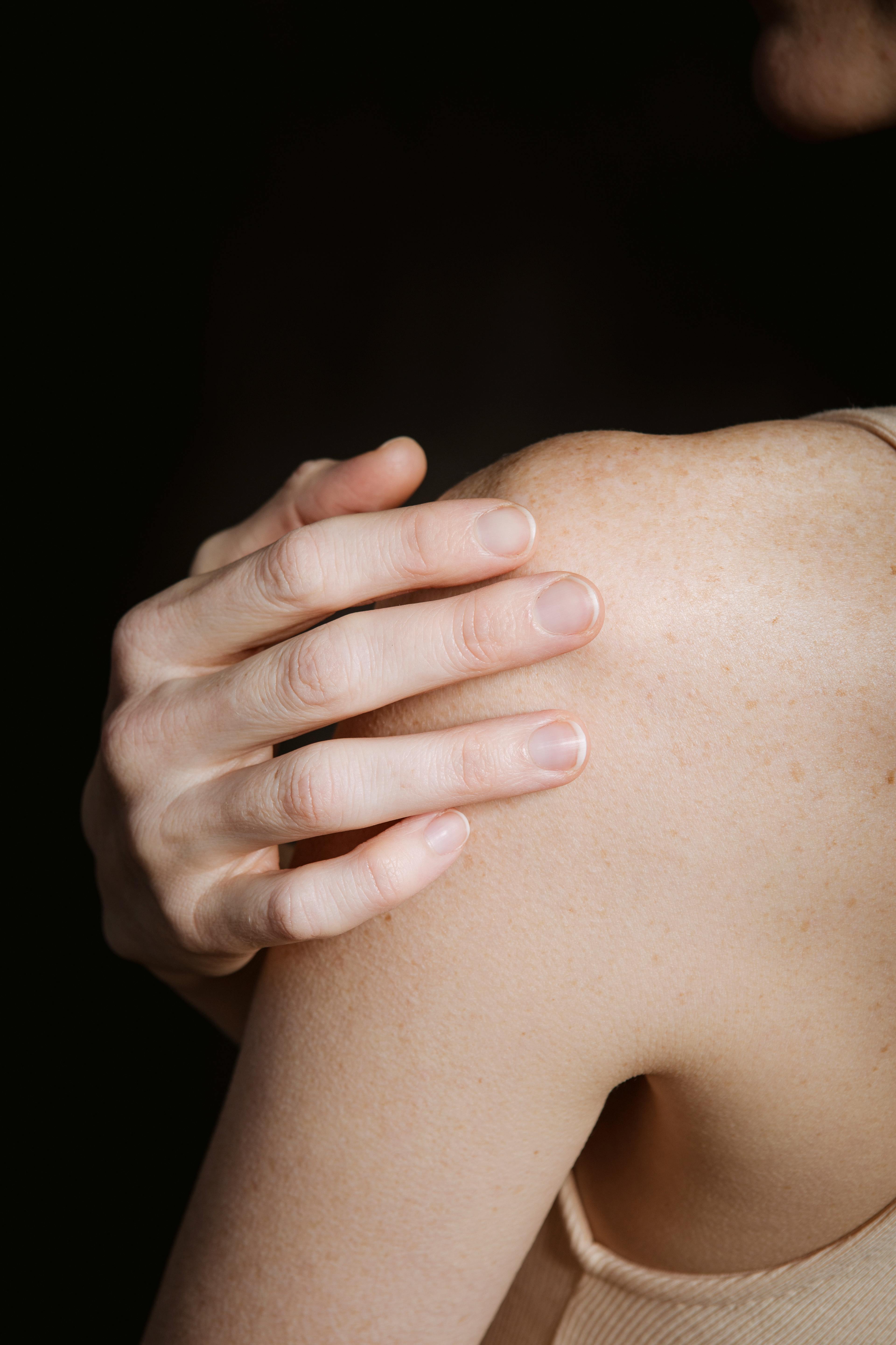 Slim female touching shoulder against dark background · Free Stock Photo