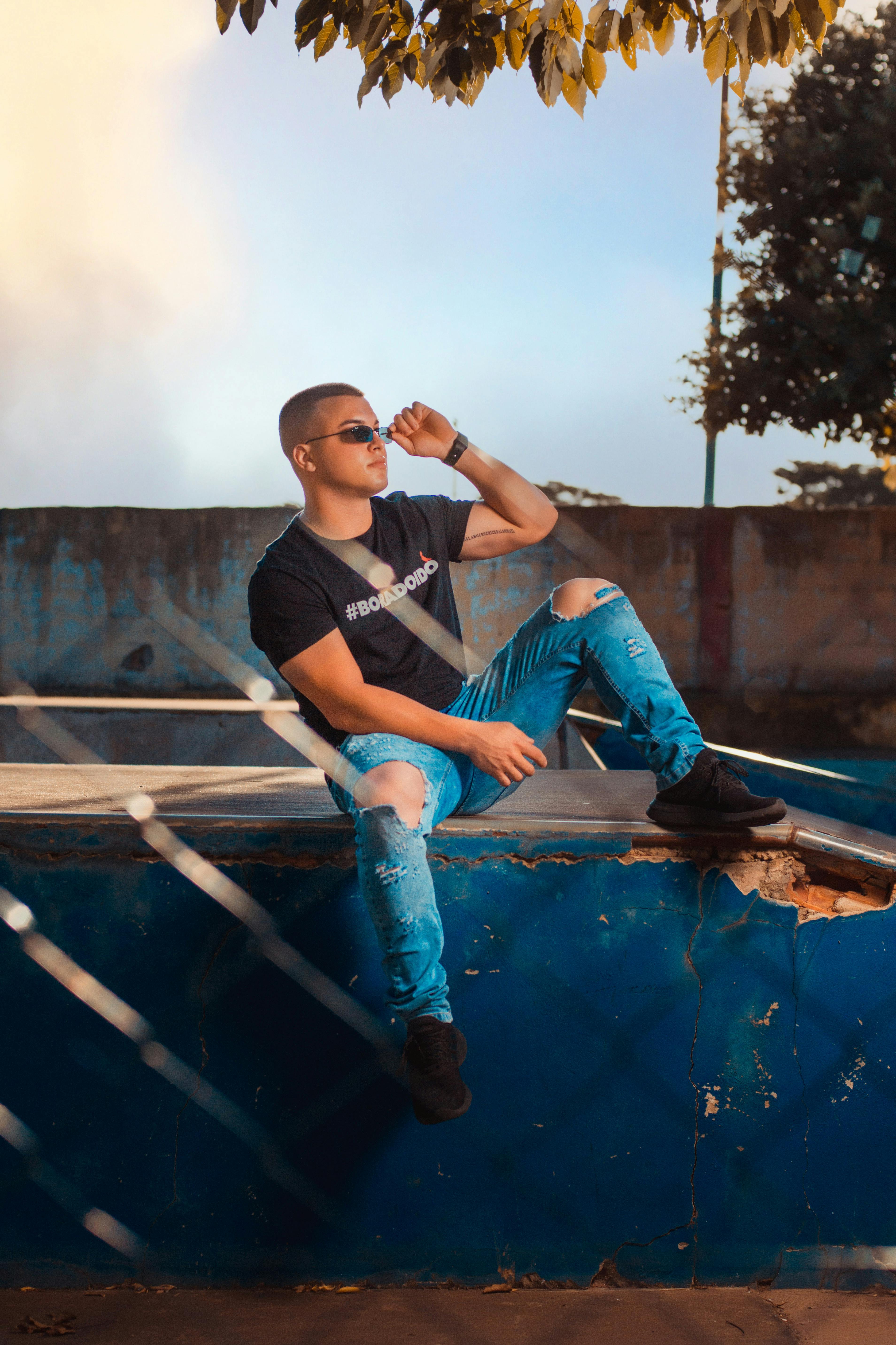 Man in Black Shirt Sitting on Concrete Railing · Free Stock Photo