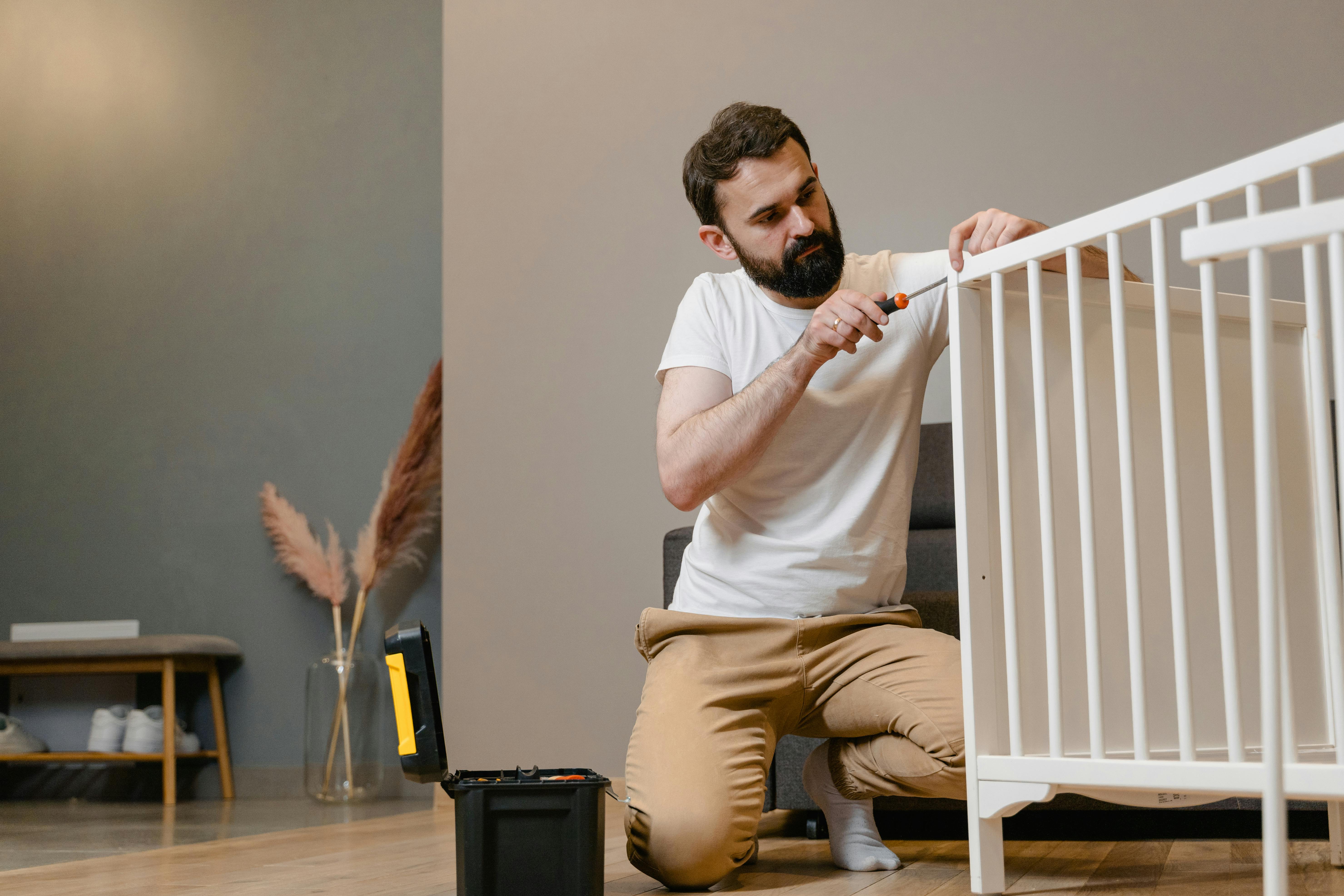 A Bearded Man in White Shirt Fixing a White Crib while Holding a ...
