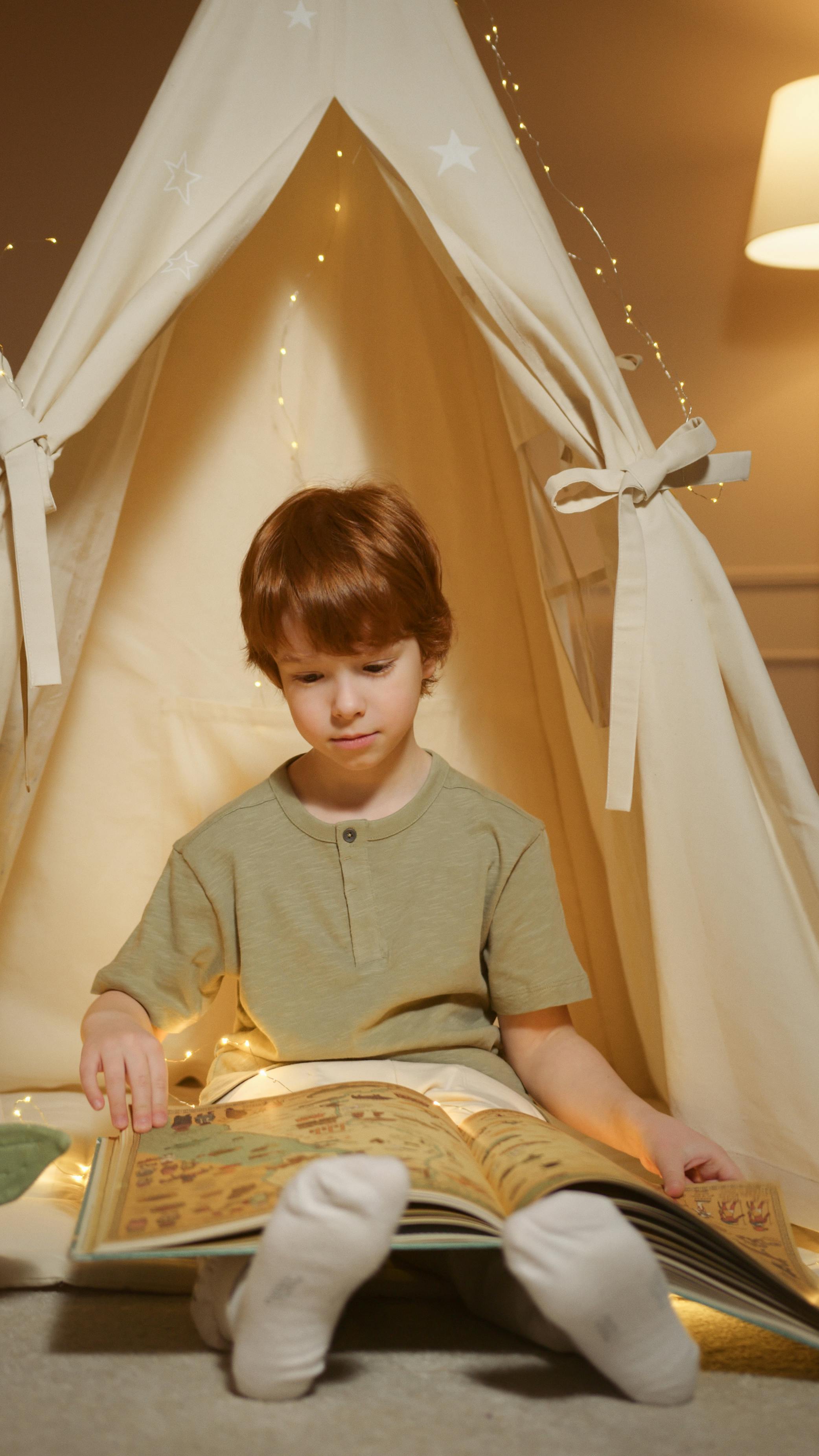 A Boy Reading a Book while Sitting in an Indoor Tent · Free Stock Photo