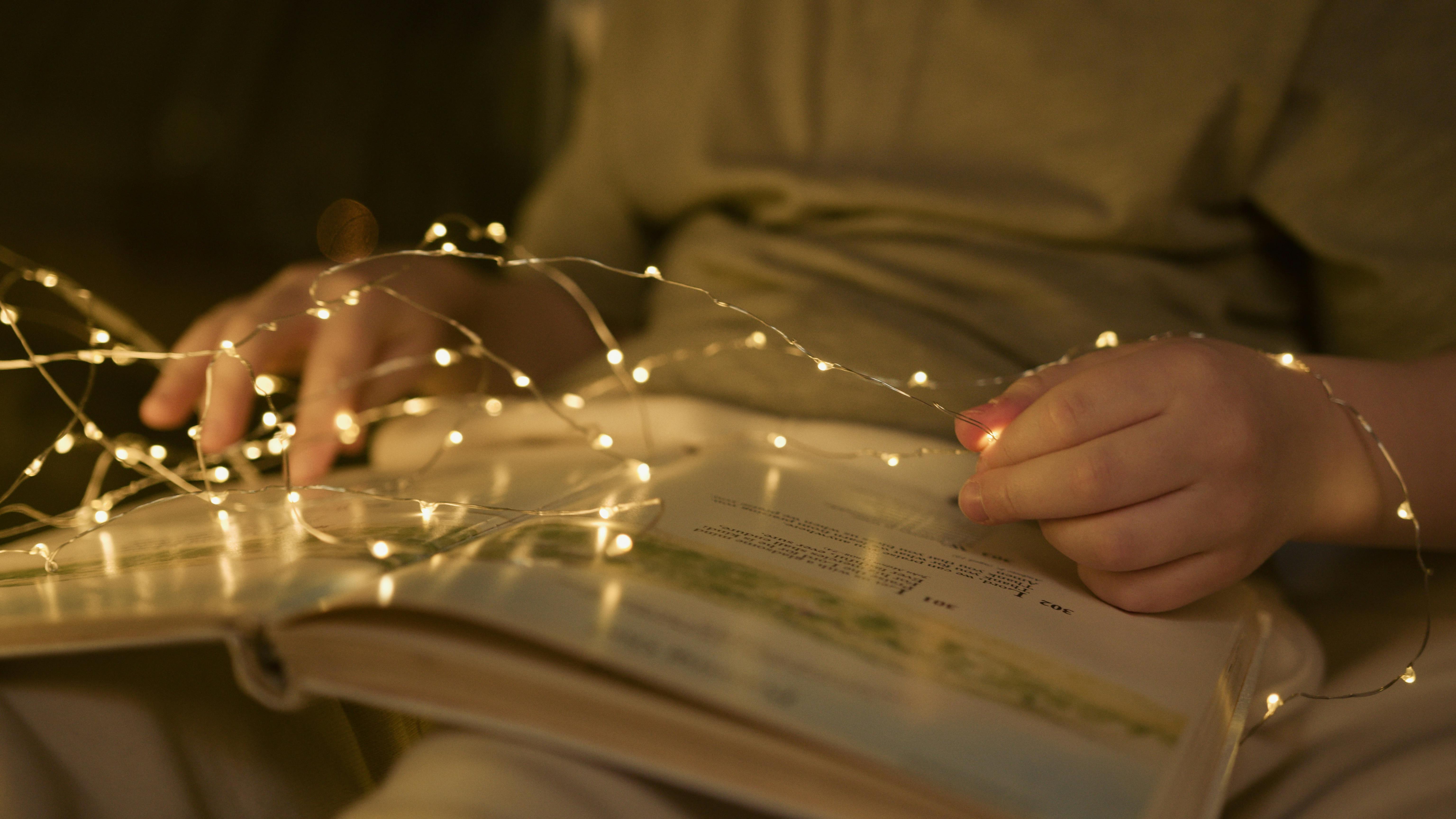 Person Holding Illuminated String Lights While Reading A Book · Free ...