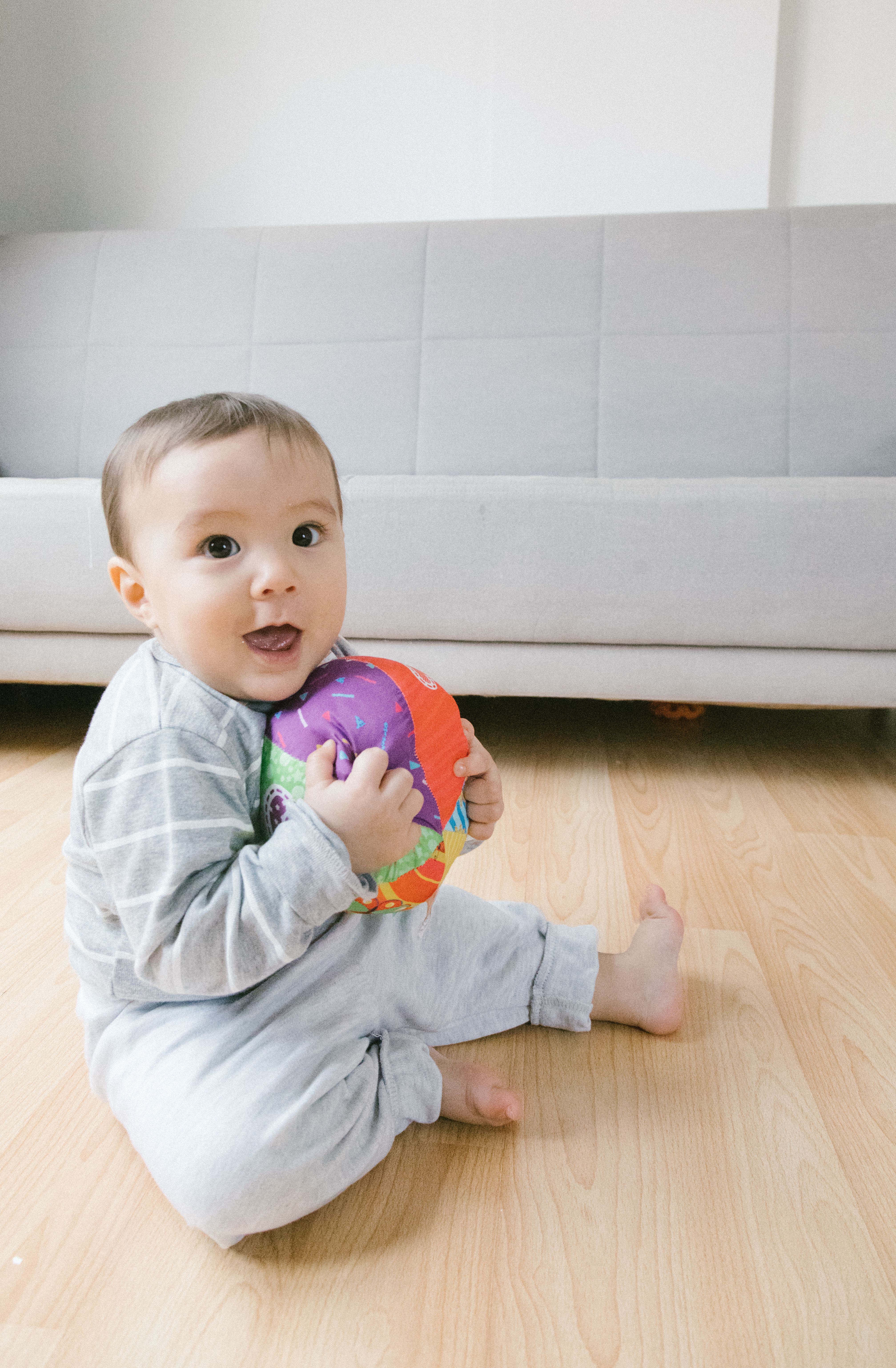 Child Holding a Ball Sitting on Wooden Floor · Free Stock Photo