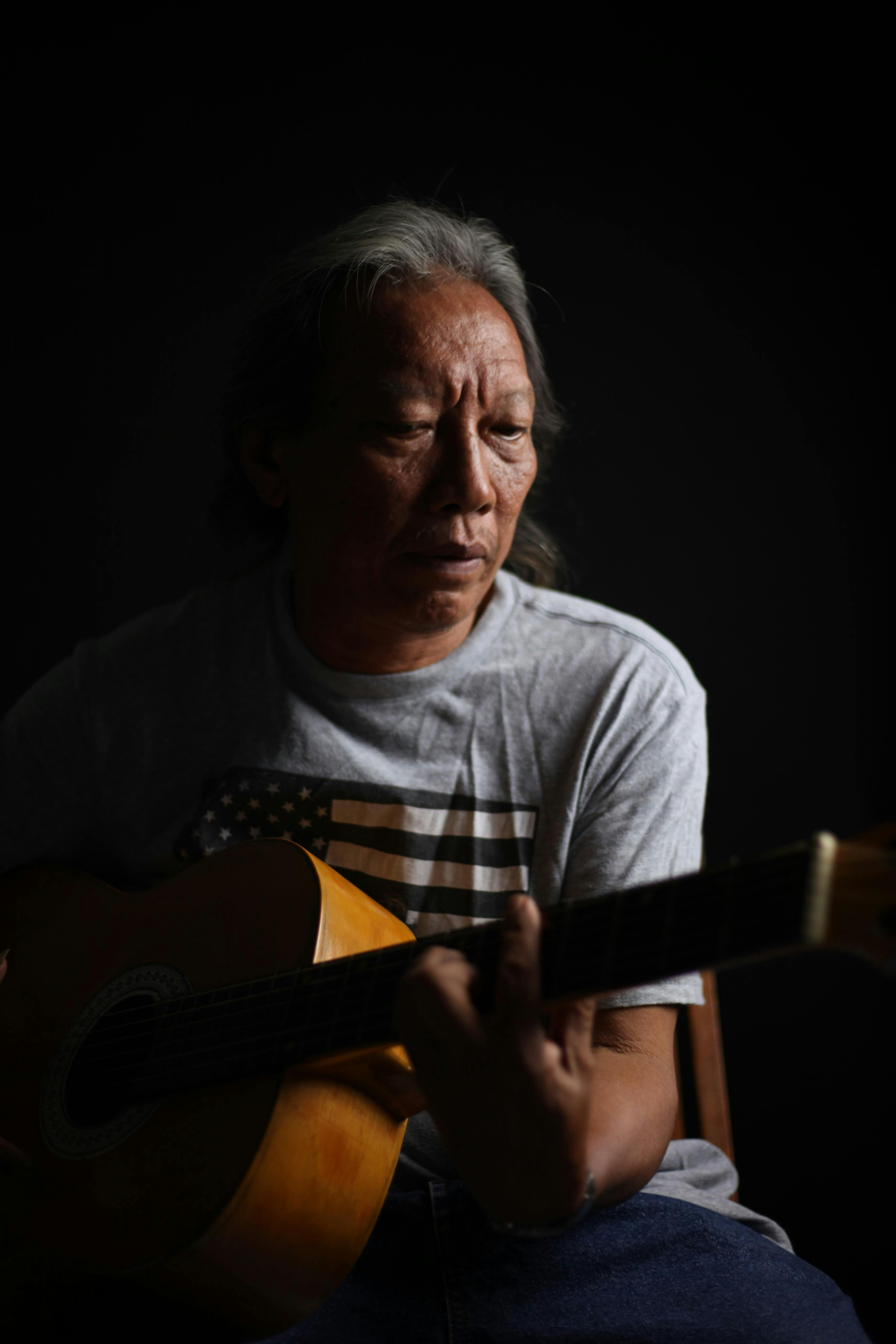 Senior Native American man playing guitar in darkness · Free Stock Photo
