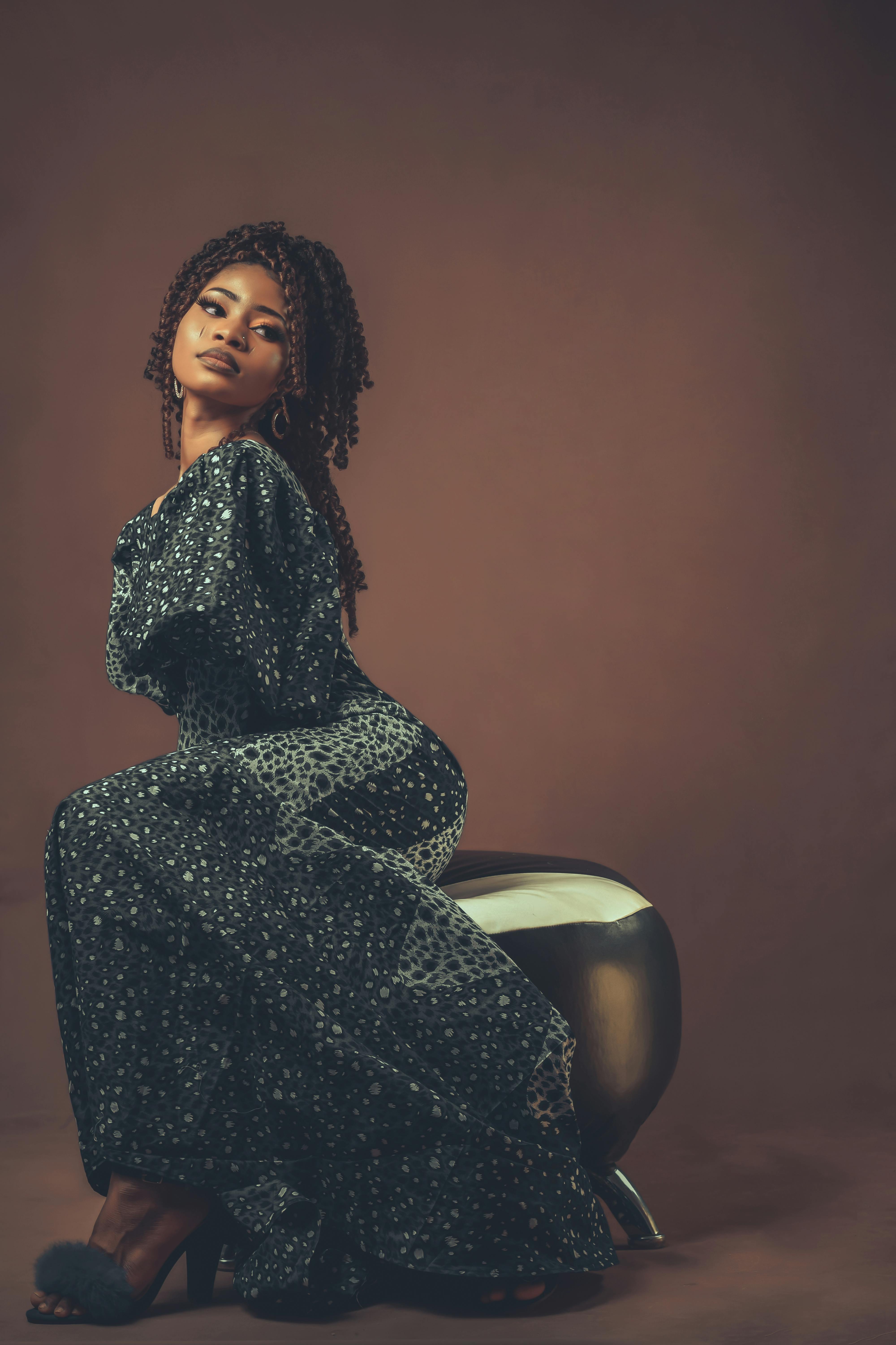 Black model in stylish dress standing near table with cosmetics in room ...
