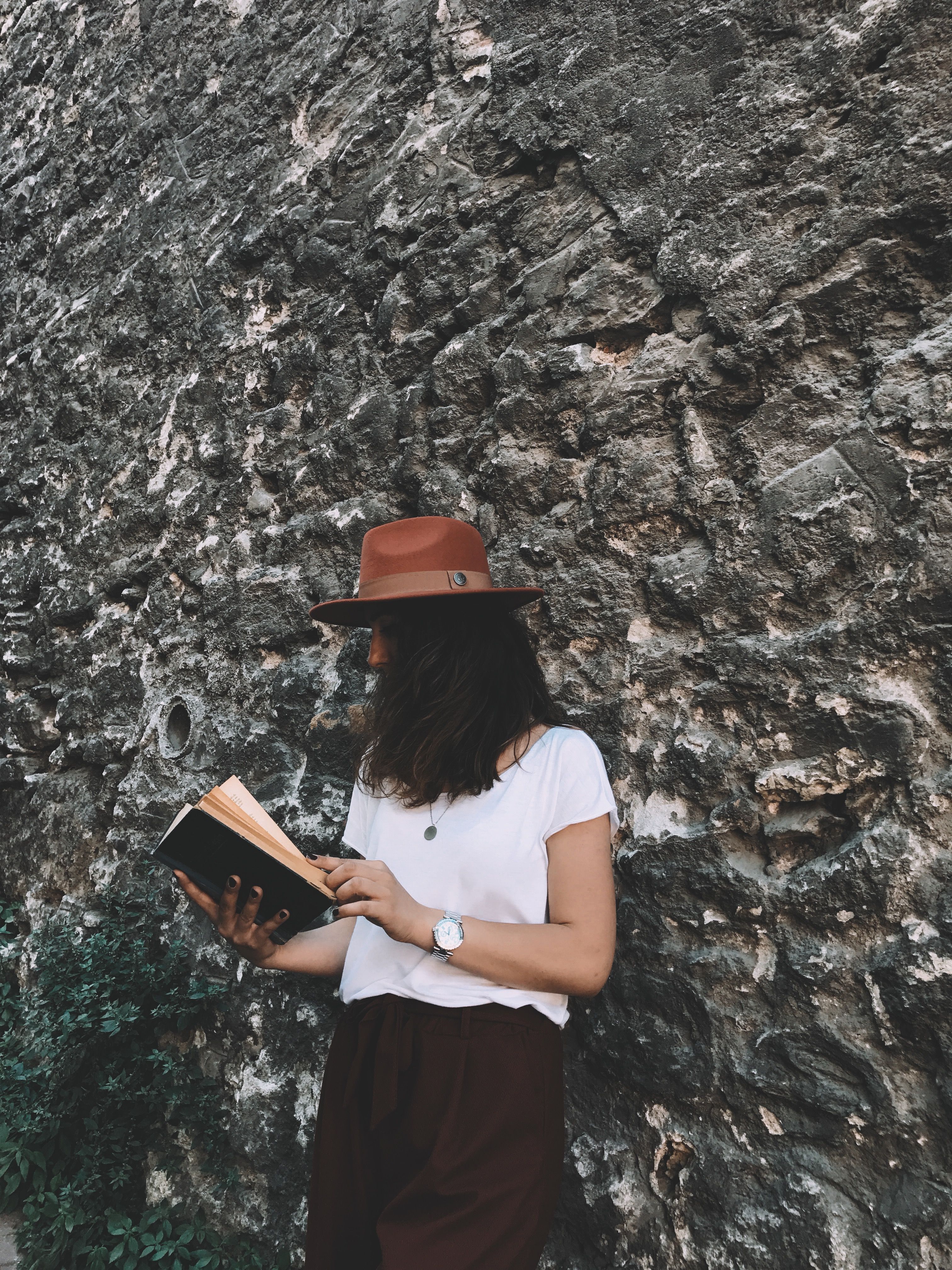 Anonymous woman reading book near stone wall · Free Stock Photo