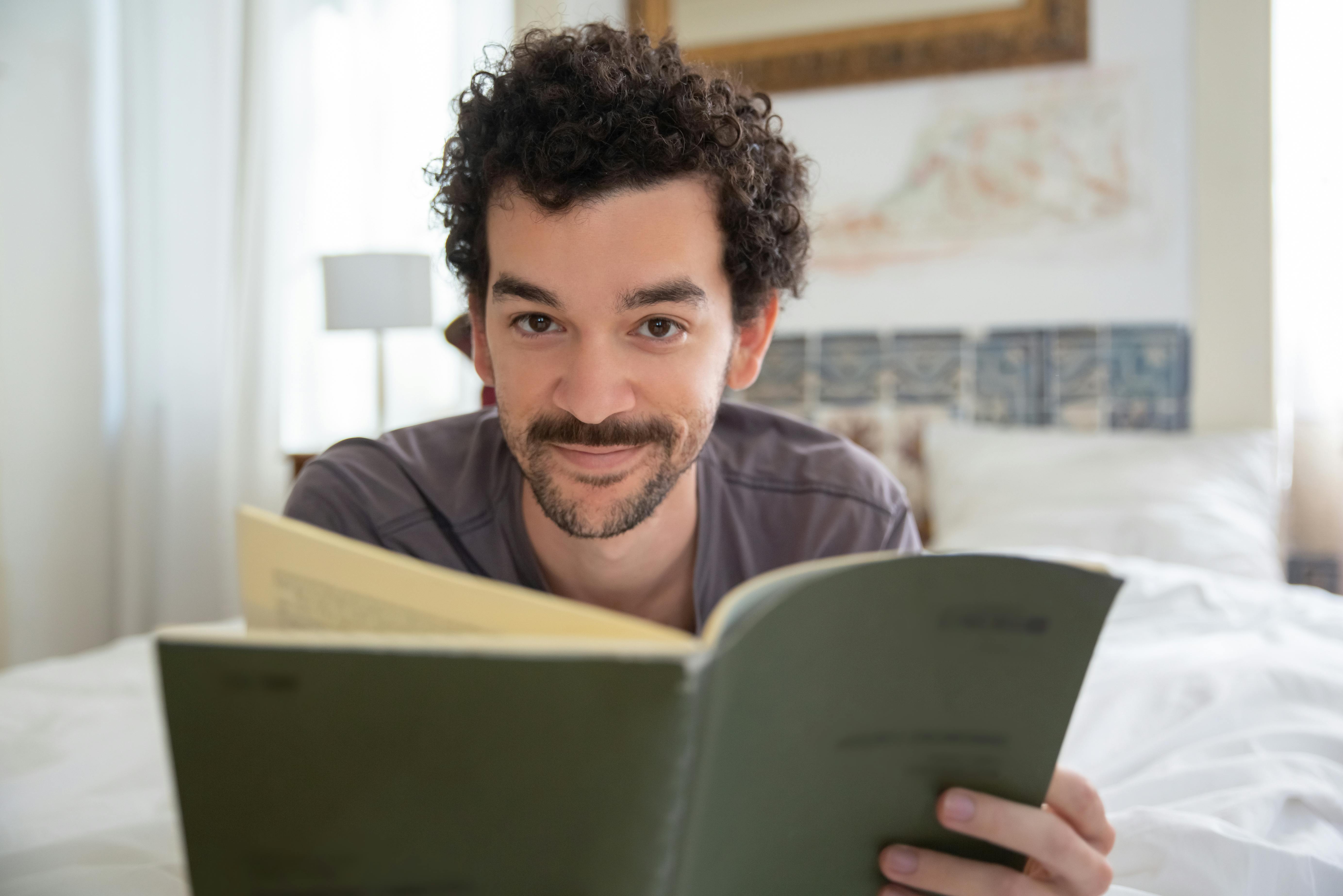 A Man Reading Book while Sitting on a Bed · Free Stock Photo