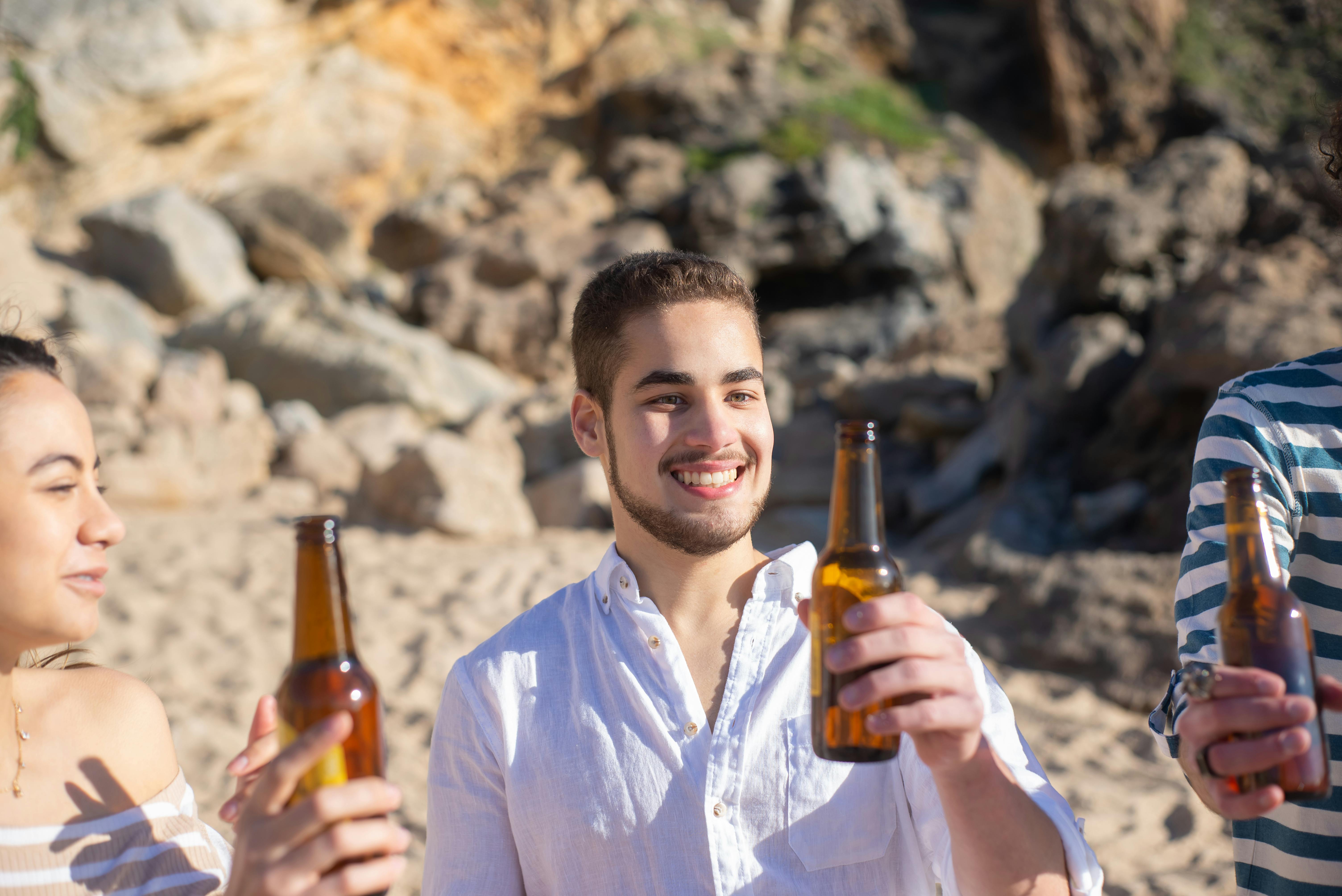 A Man Smiling while Holding a Bottle of Beer · Free Stock Photo