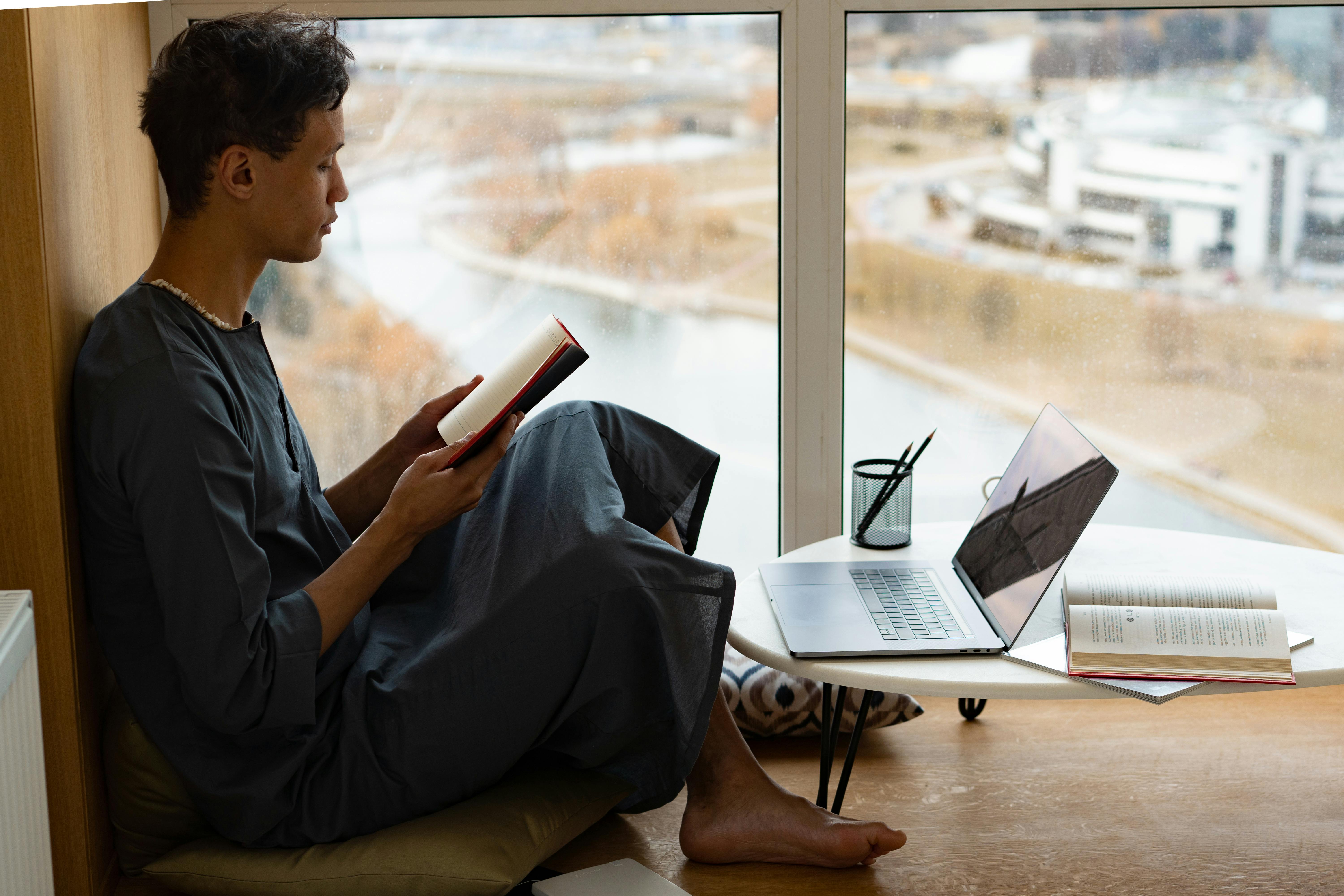 Man Sitting By the Window Reading a Book · Free Stock Photo