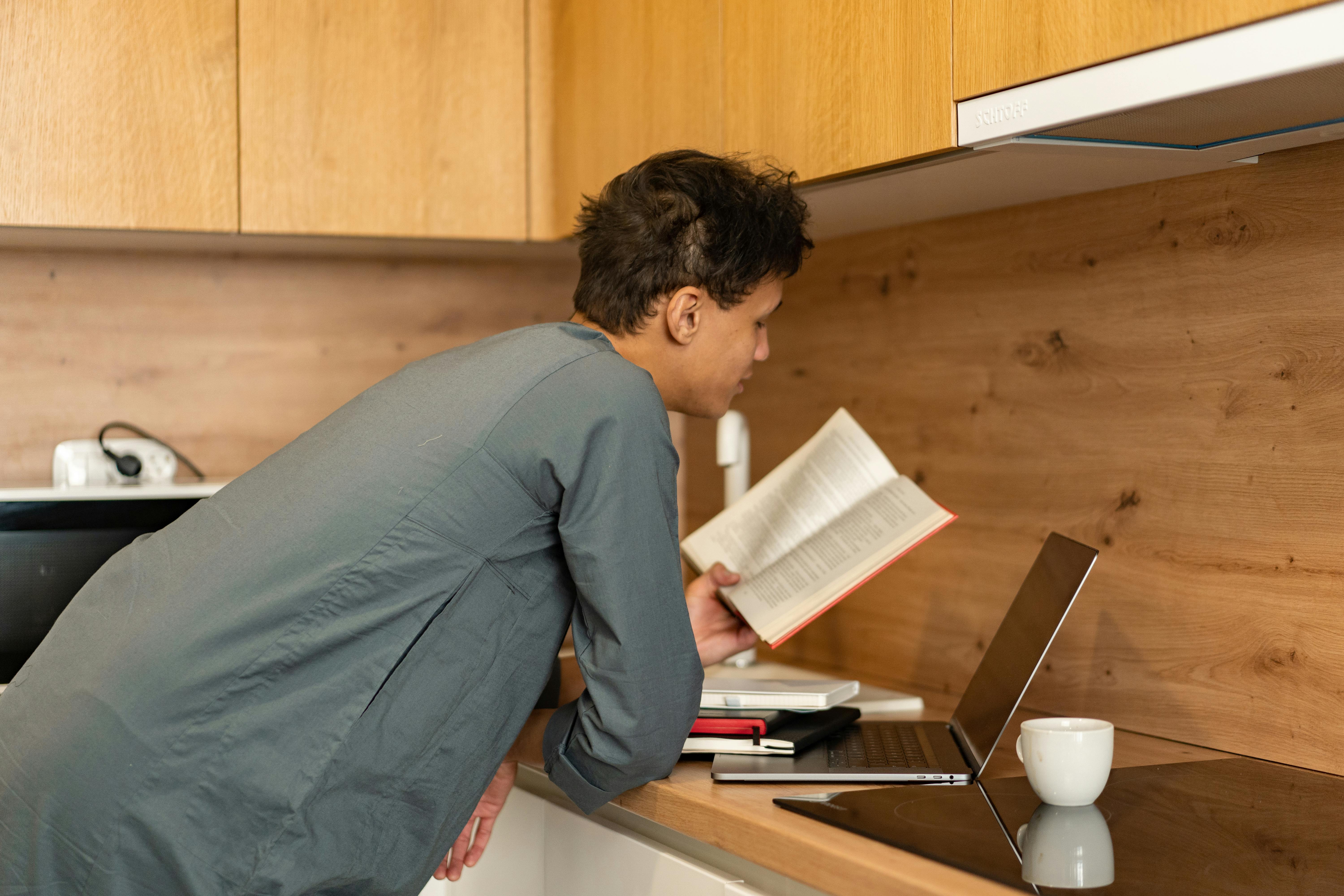 Man Reading a Book in Front of a Laptop · Free Stock Photo