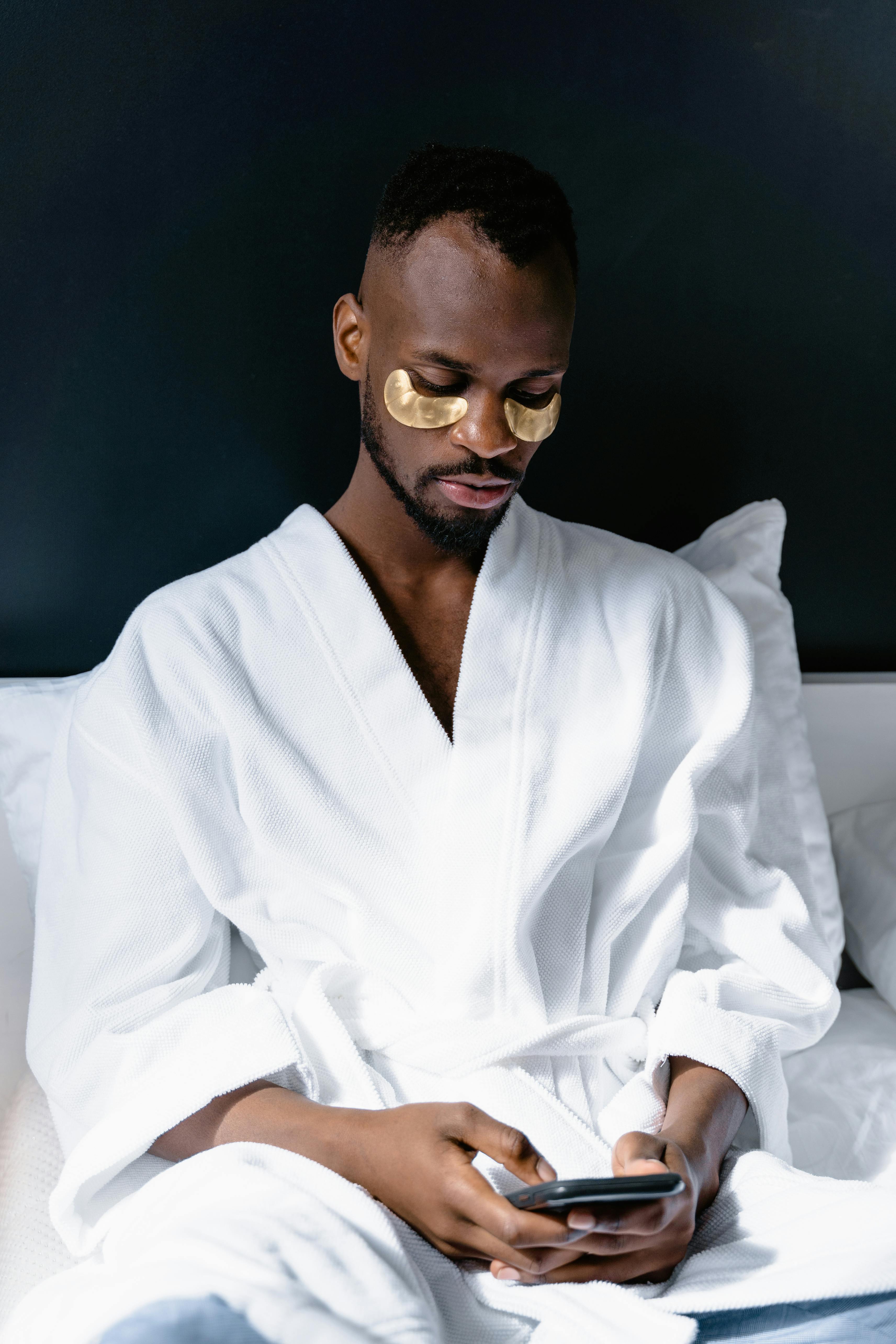 A Man in White Robe Sitting while Using a Smartphone · Free Stock Photo