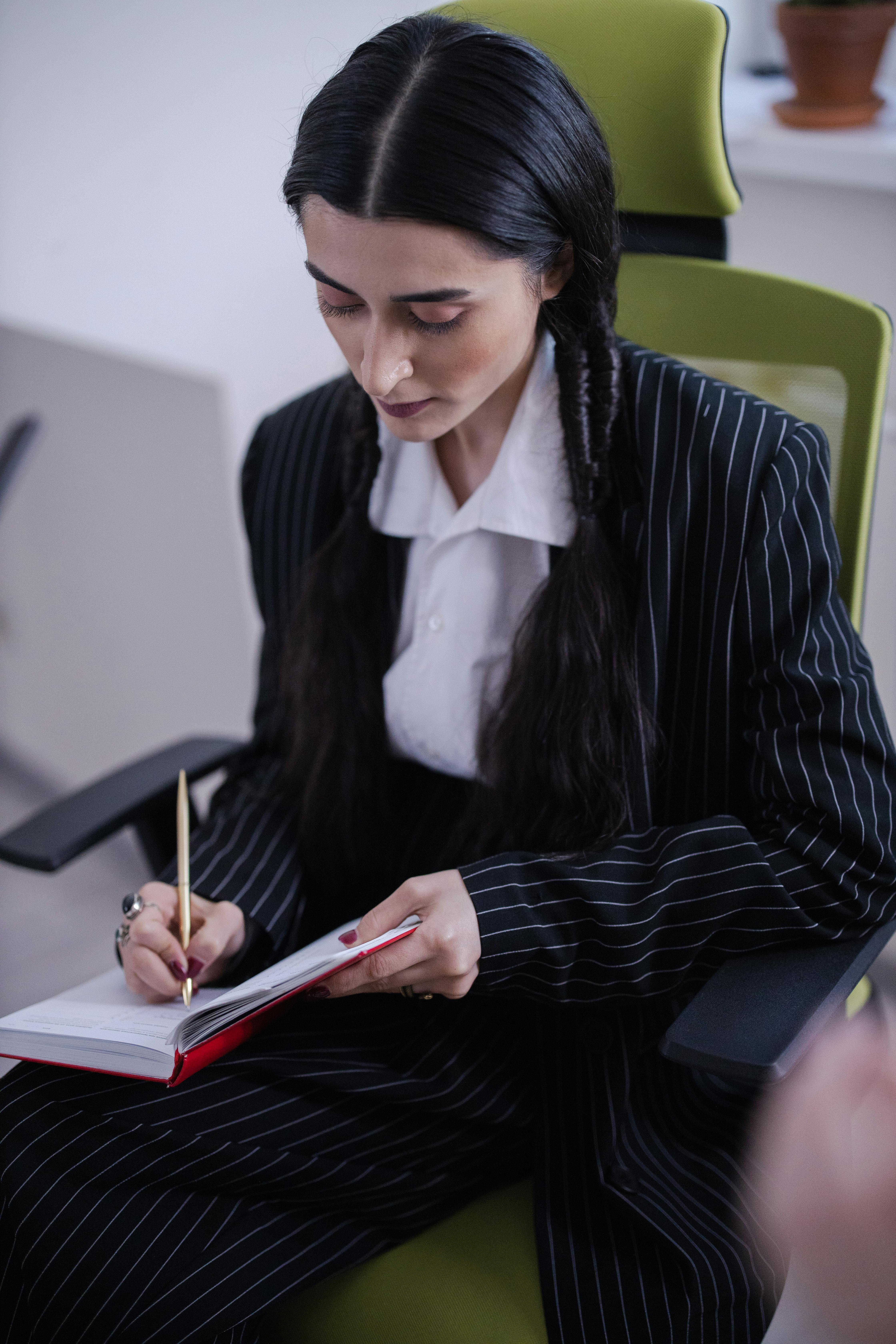 A Woman in Black Blazer Sitting while Taking Notes · Free Stock Photo