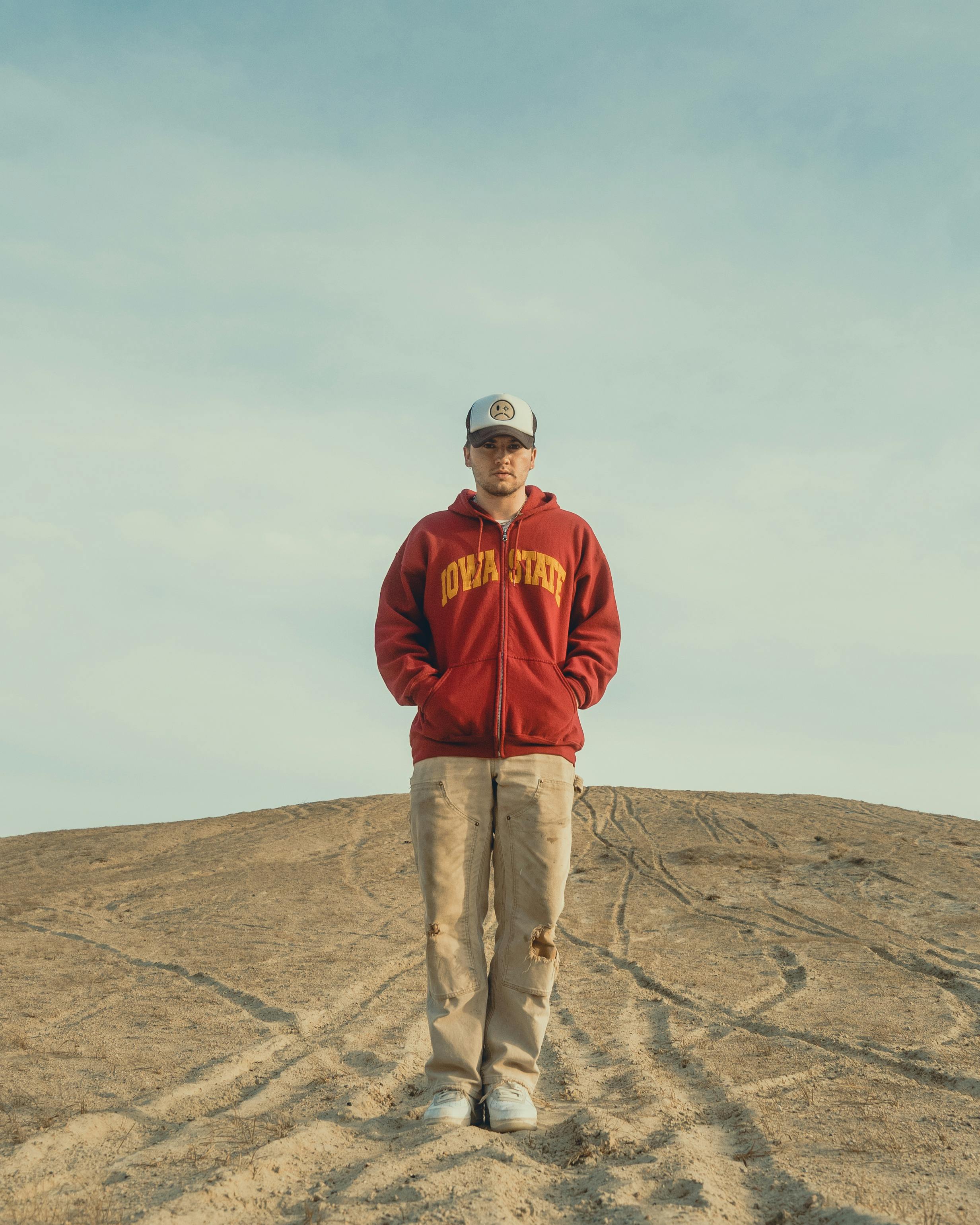 Man in Red Jacket and Ripped Jeans Standing on Sand · Free Stock Photo