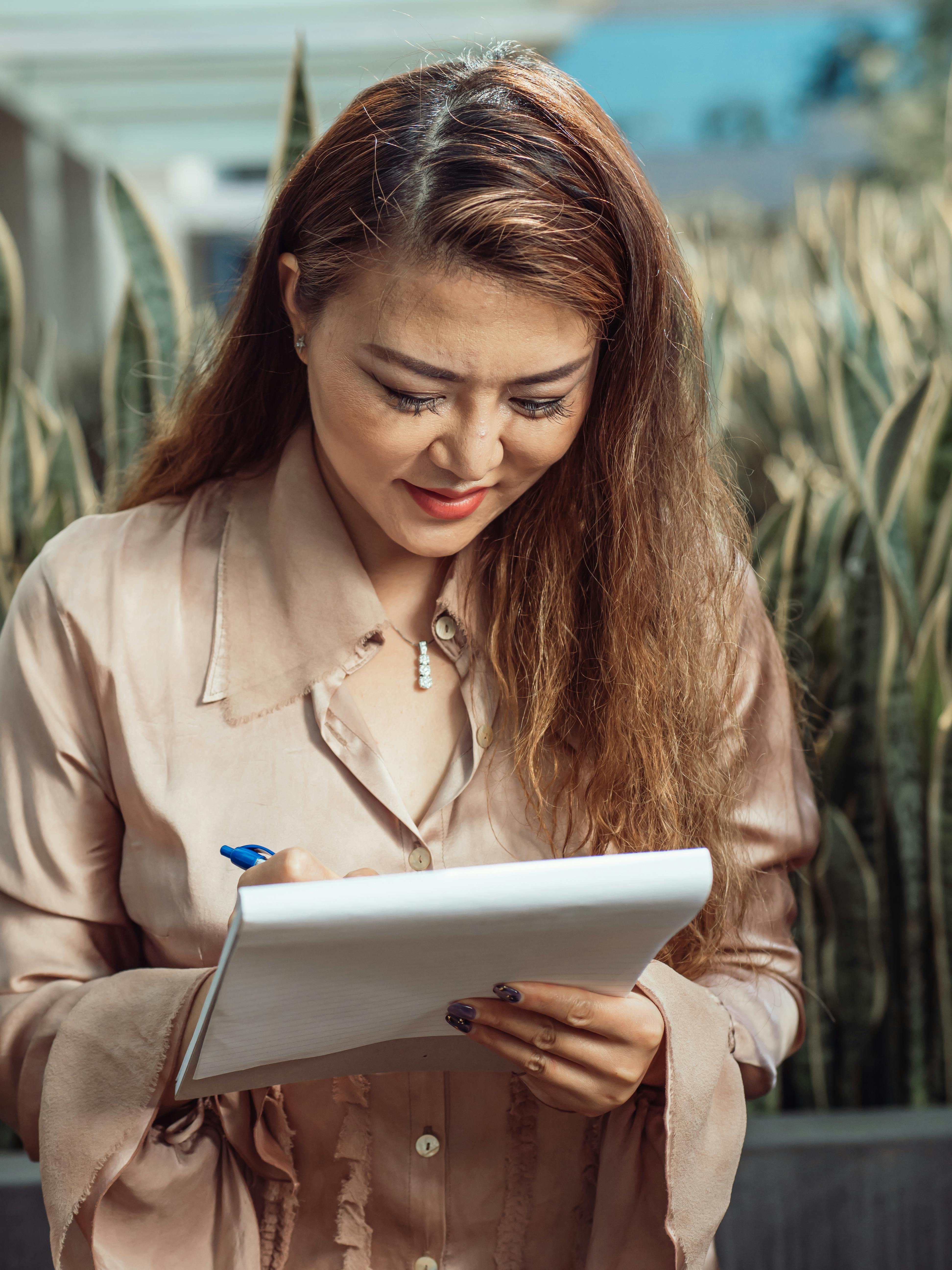 A Woman in Brown Long Sleeves Smiling While Writing on the Paper · Free ...