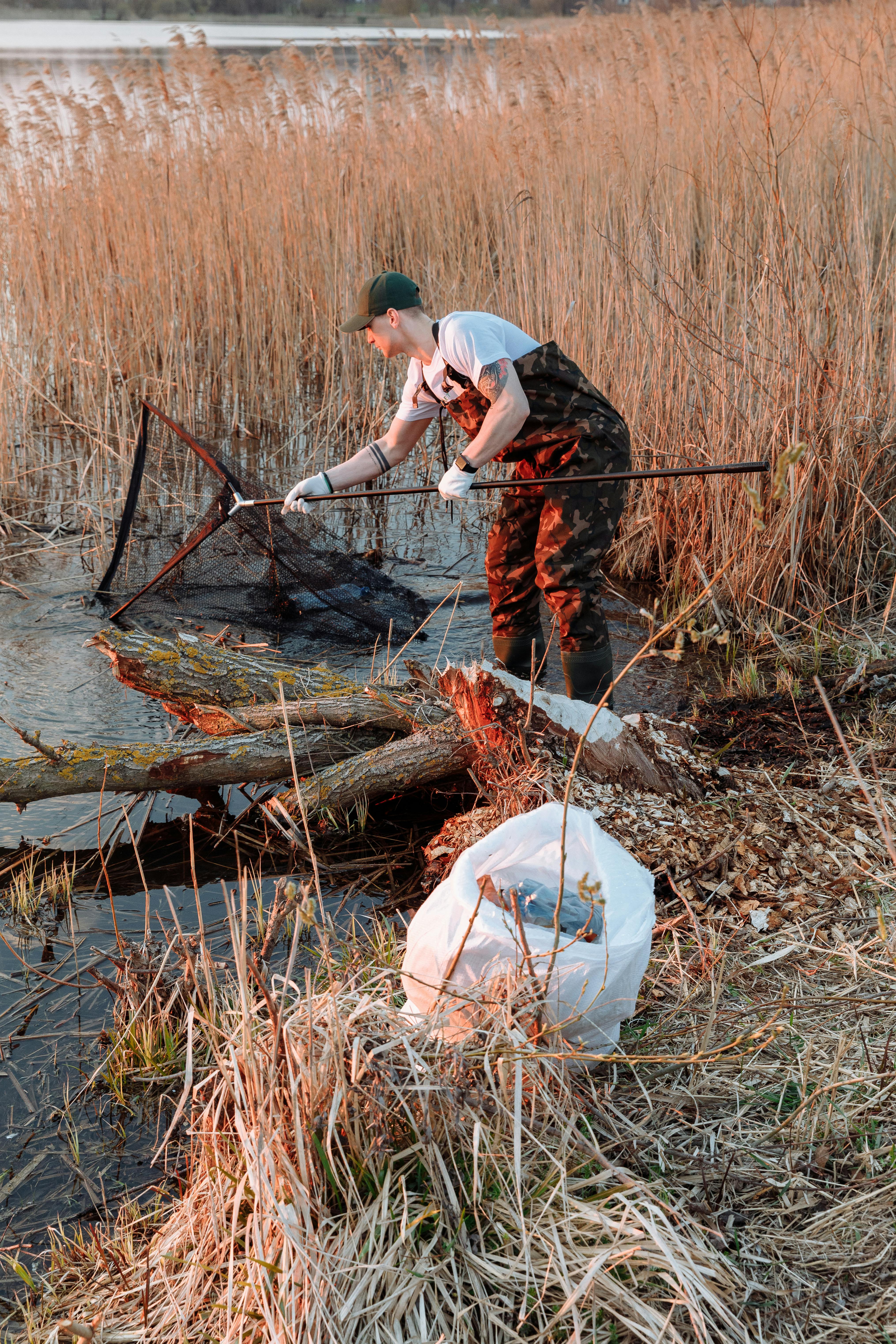 A Man using a Net while Collecting Garbage in the River · Free Stock Photo