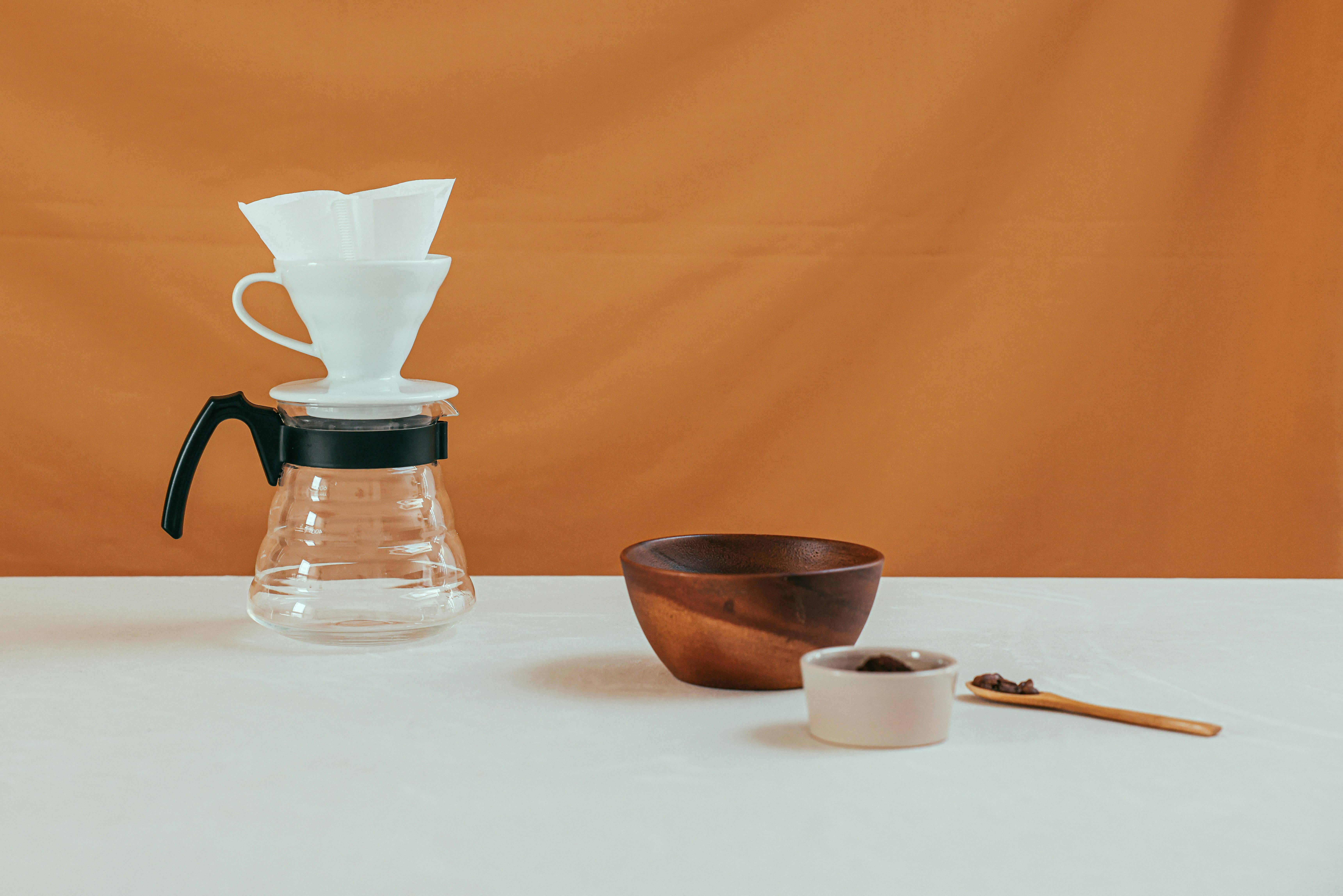 A Glass Pour-Over Coffee Maker on a White Surface Beside a Wooden Bowl ...