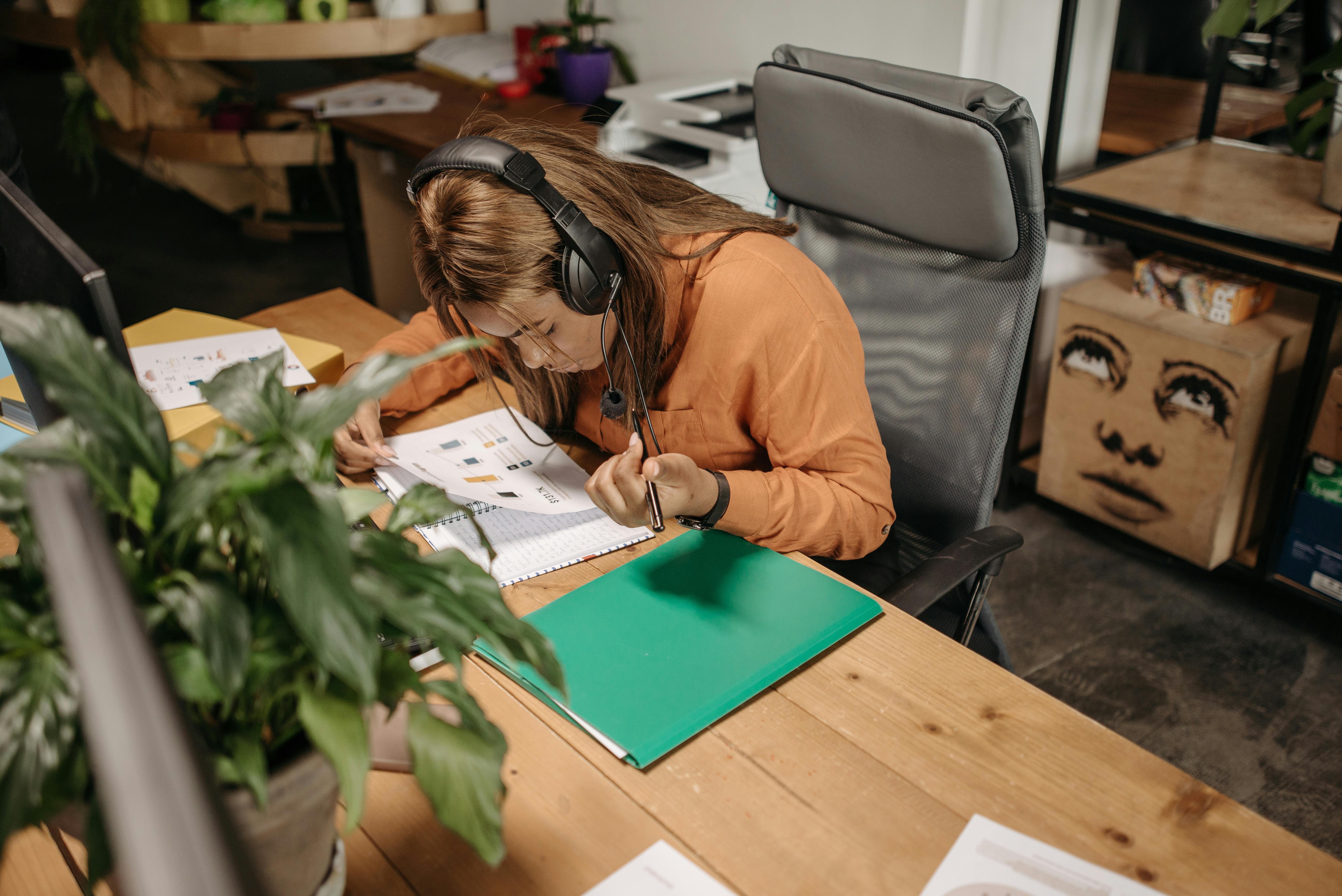 A Woman Reading a Document in front of Her Computer Desk · Free Stock Photo