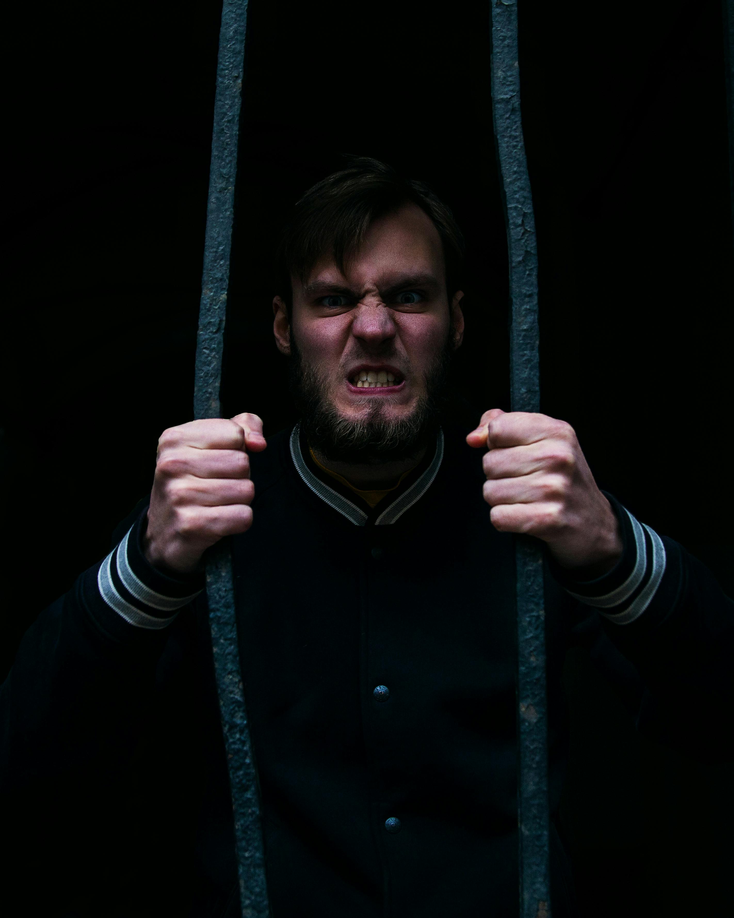 An Angry Man in Black Jacket Standing Behind Metal Bars · Free Stock Photo