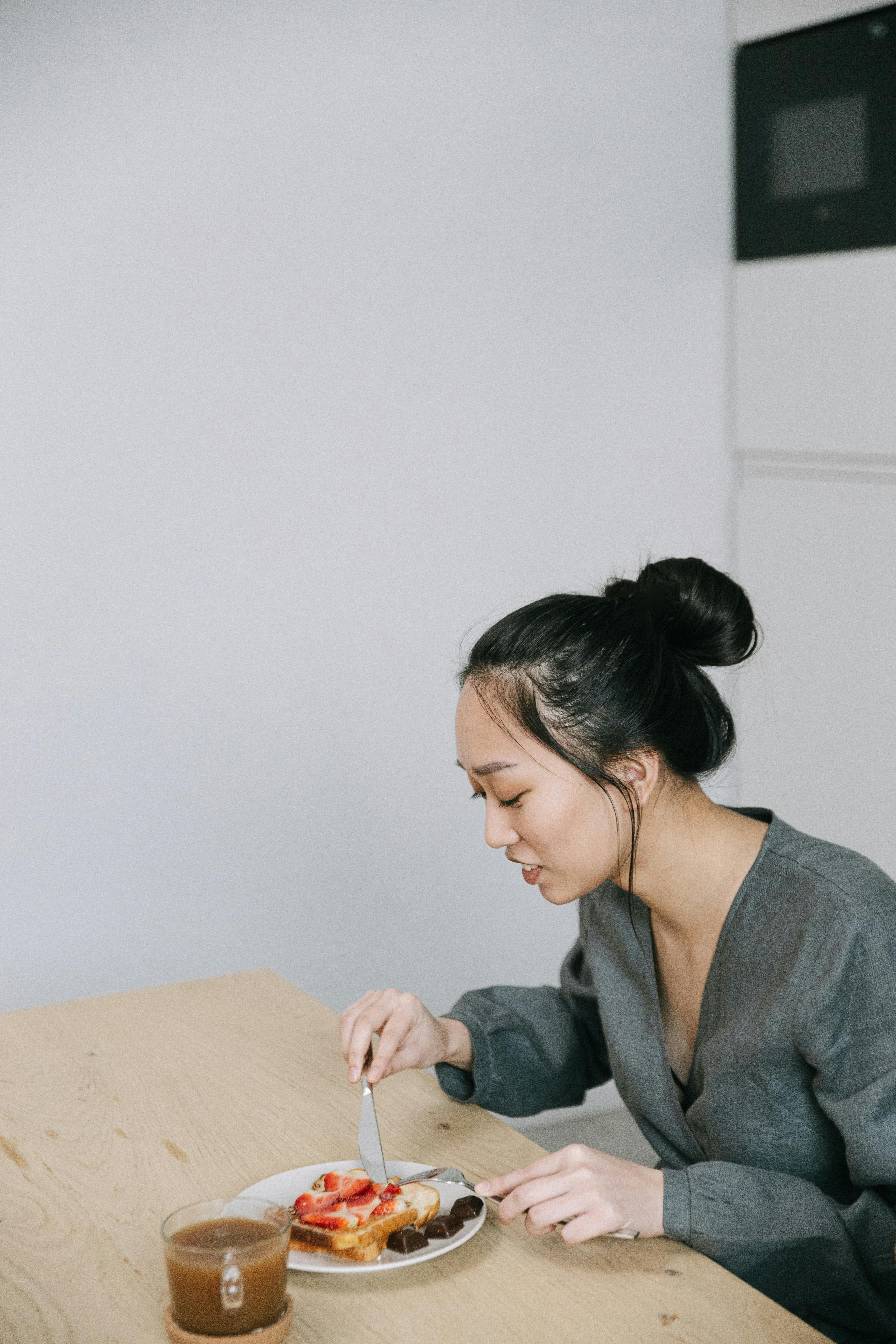 Woman in Gray Long Sleeve Dress Eating on Brown Wooden Table · Free ...