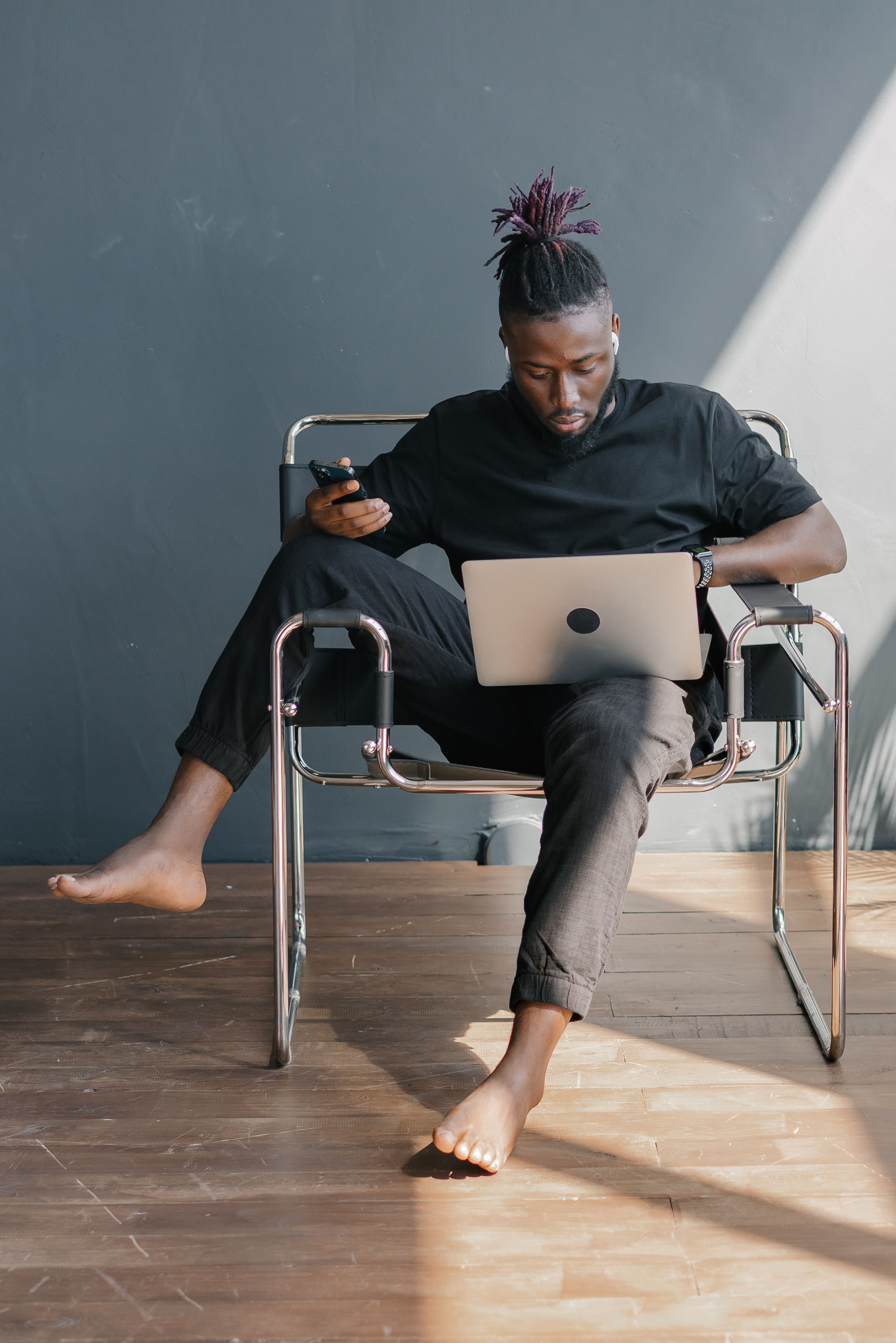Man in Black Crew Neck T-shirt and Black Pants Sitting on Chair Using ...