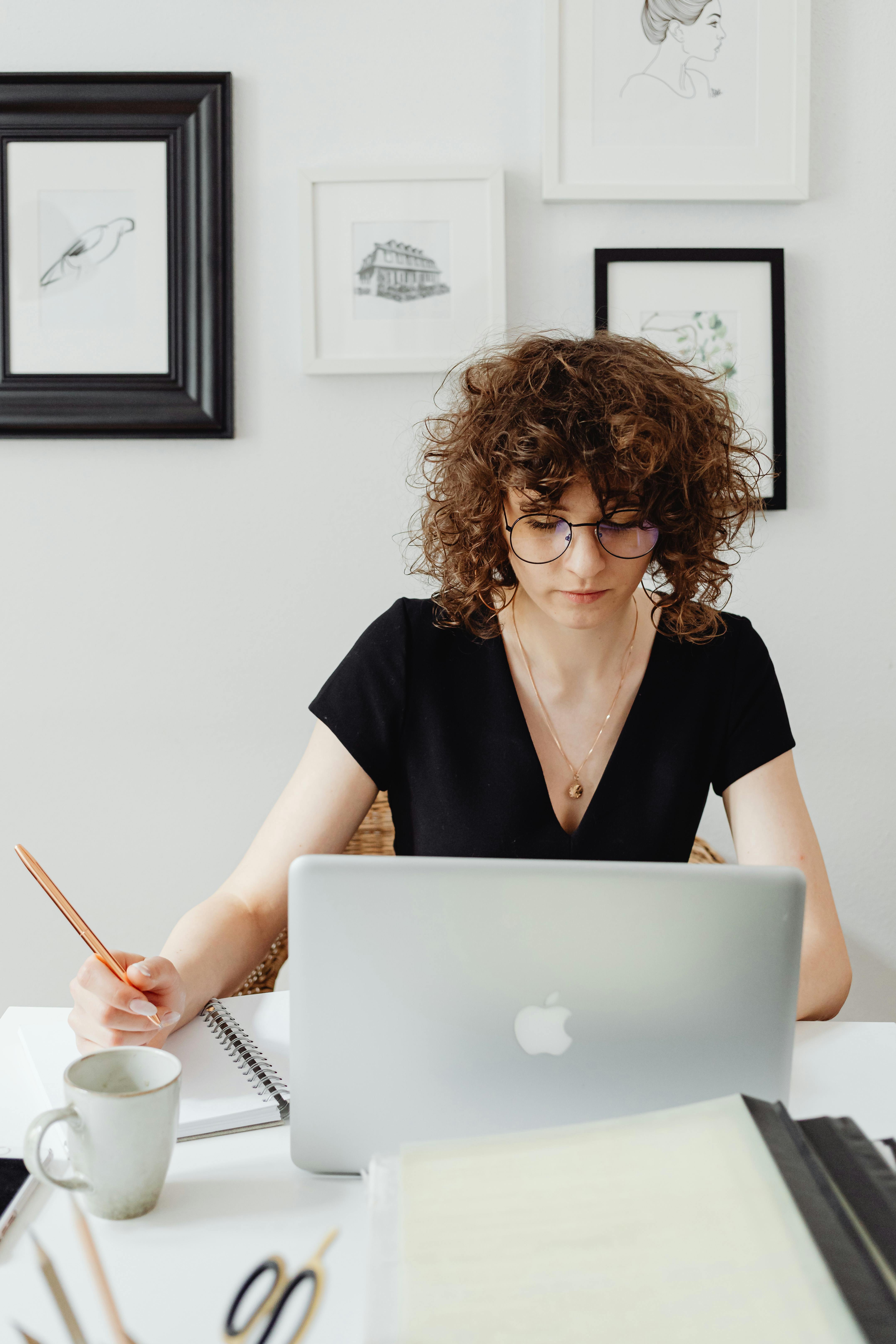 A Woman Taking Notes while Using a Laptop · Free Stock Photo