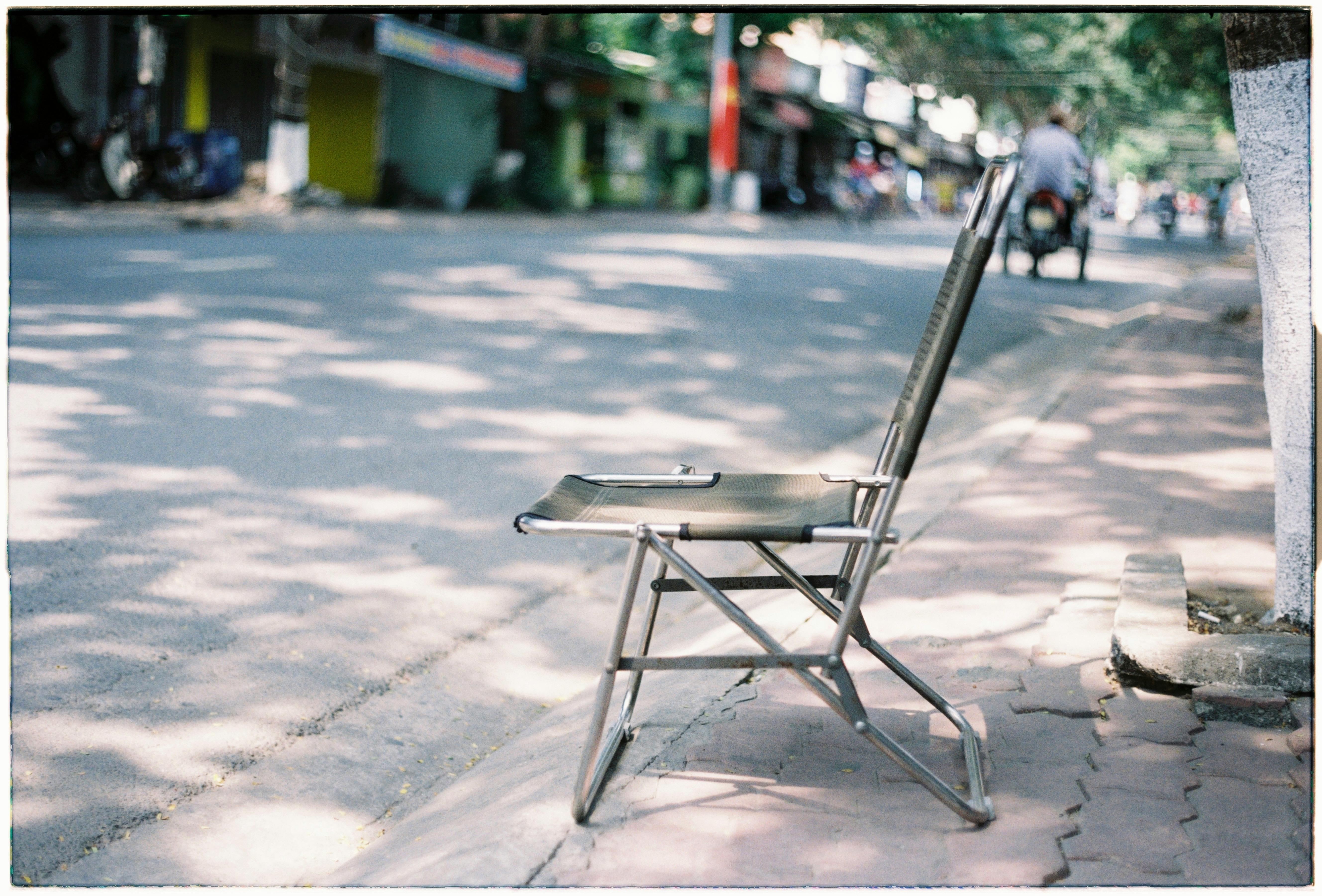 Shallow Focus Photo of Black Folding Chair on Roadside · Free Stock Photo
