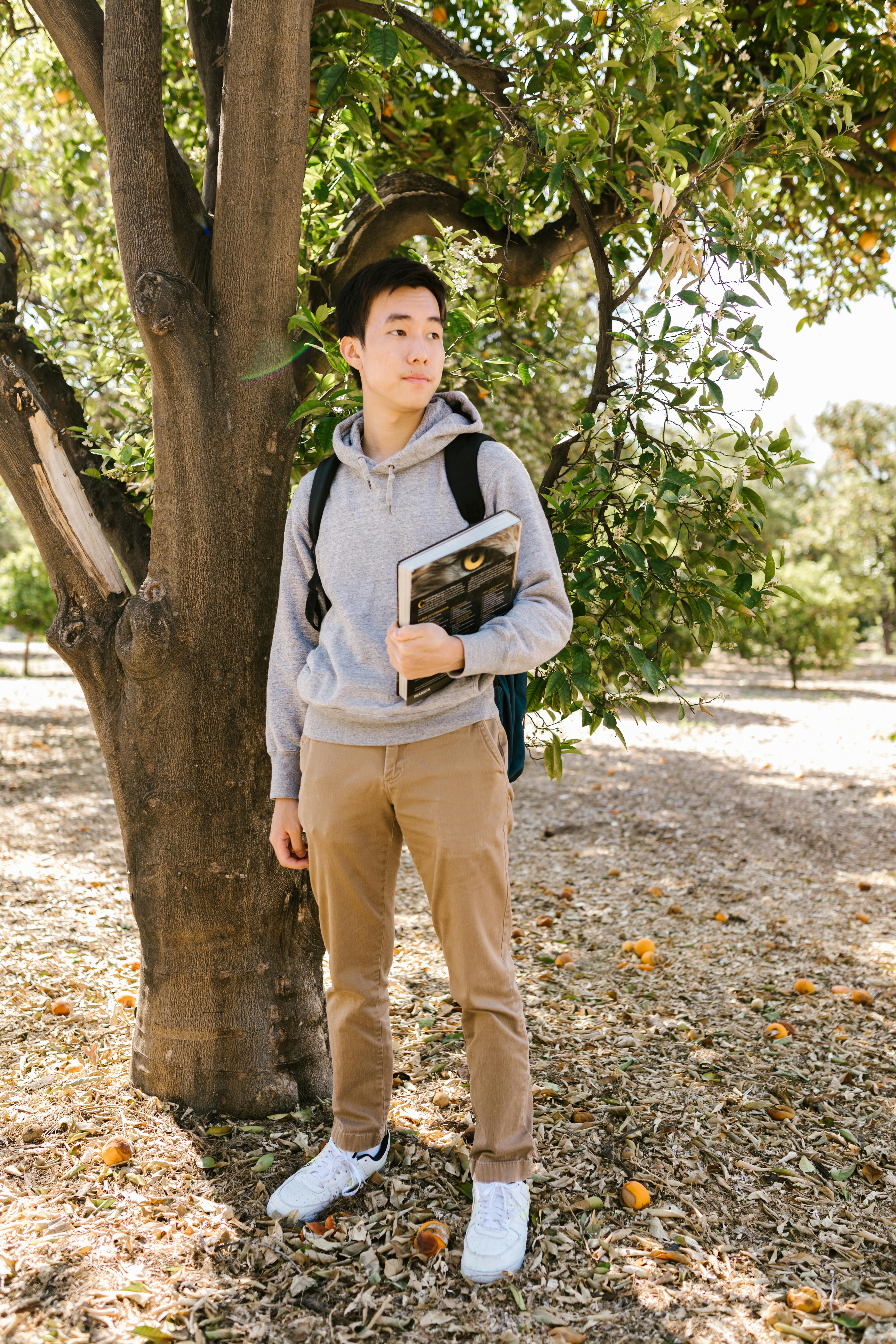 College Boy Student Standing Near the Tree while Holding a Book · Free ...