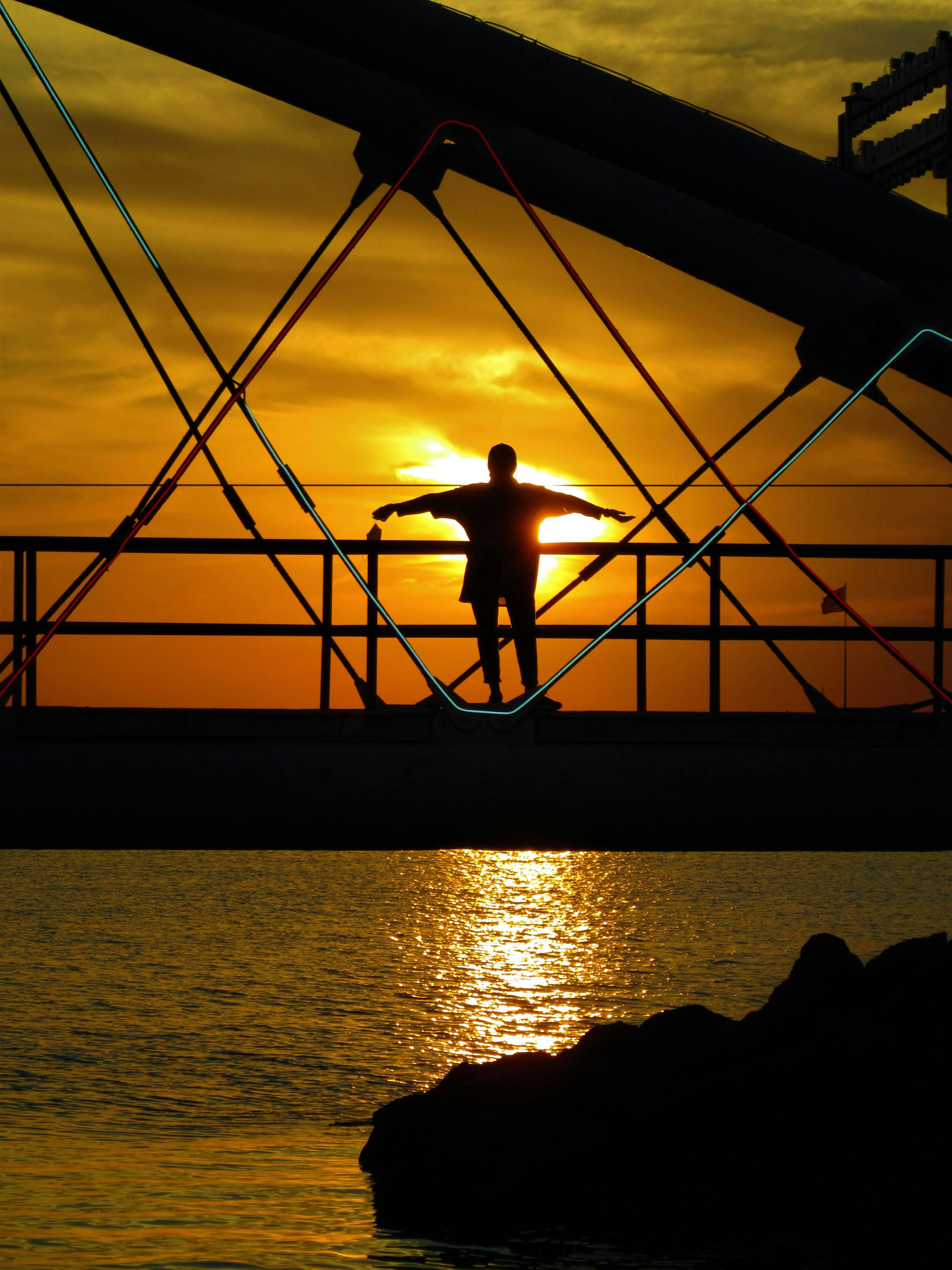 Silhouette of Person Standing on Bridge During Sunset · Free Stock Photo