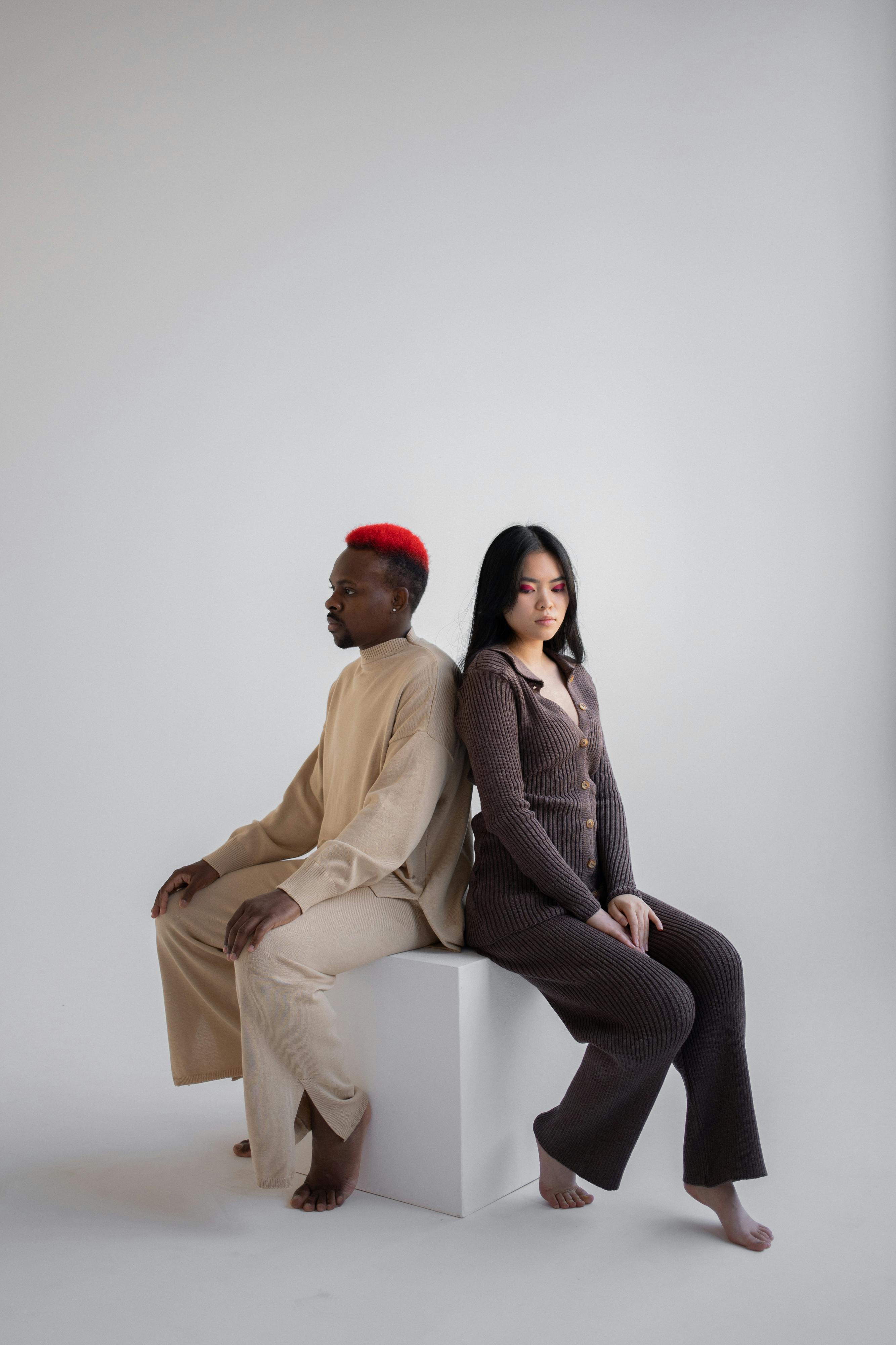 Multiracial unemotional man and woman sitting on cube · Free Stock Photo