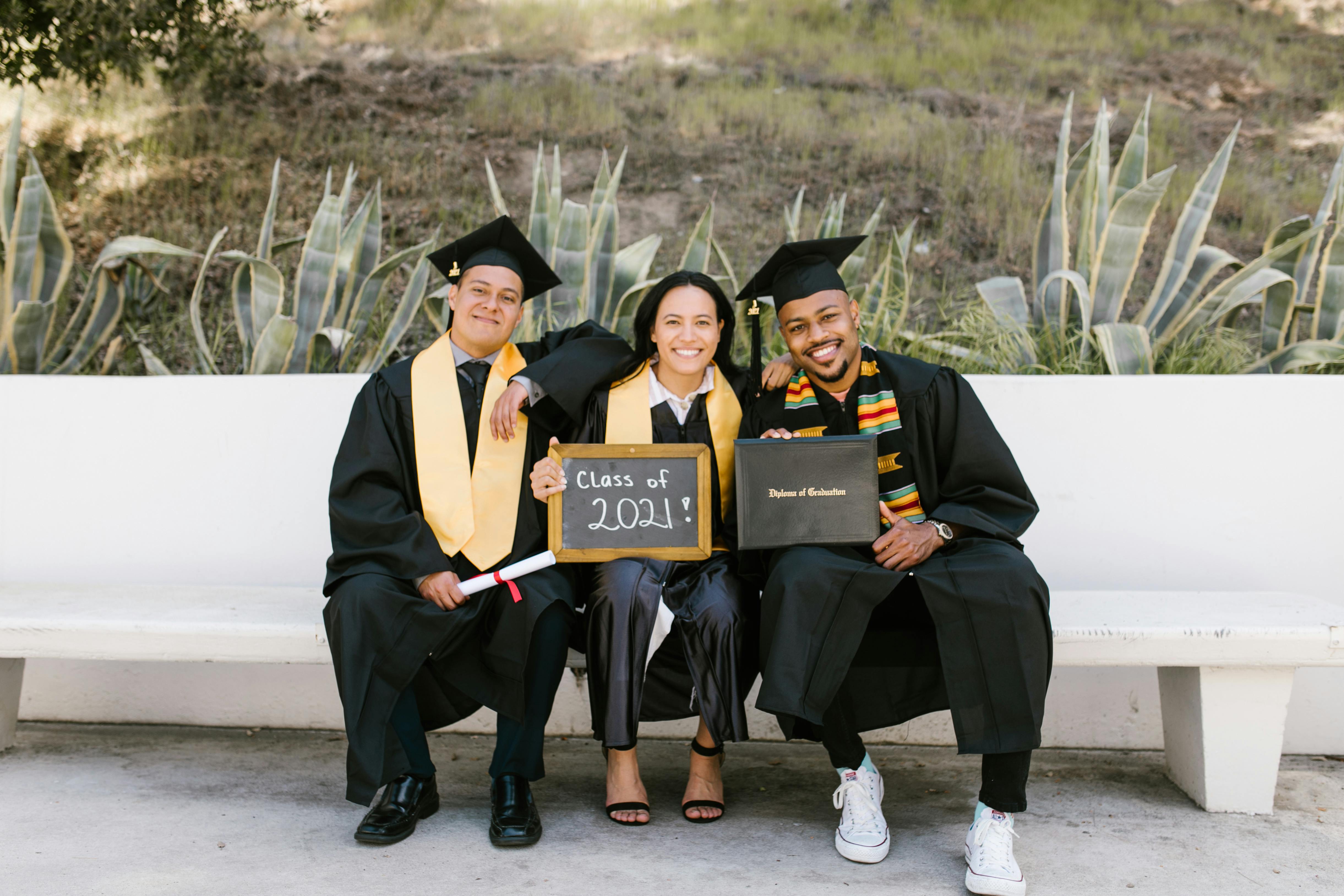 Woman and Two Men Sitting on a Bench in Graduate Gowns Smiling · Free ...