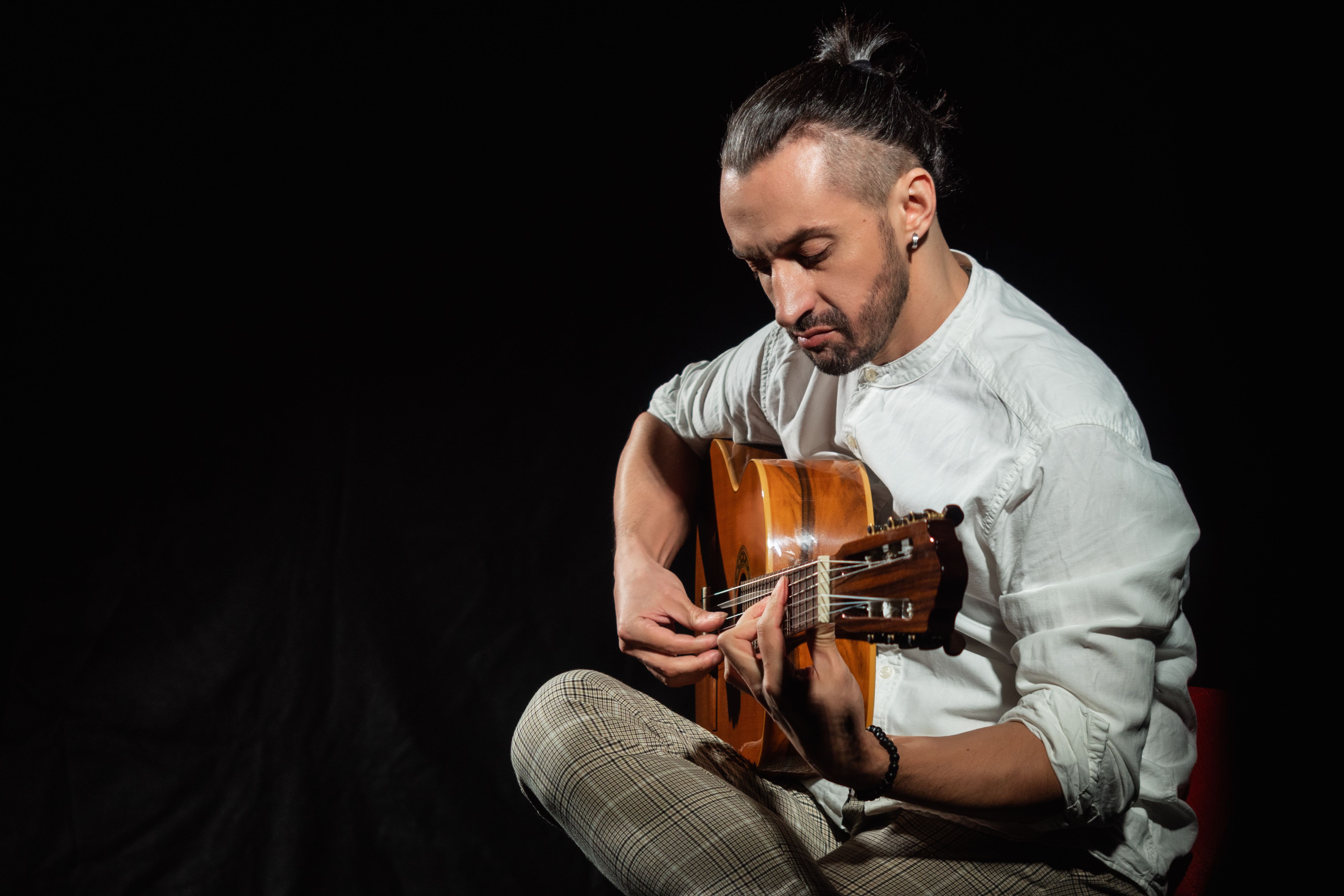 A Back View of a Person Sitting while Playing Guitar · Free Stock Photo