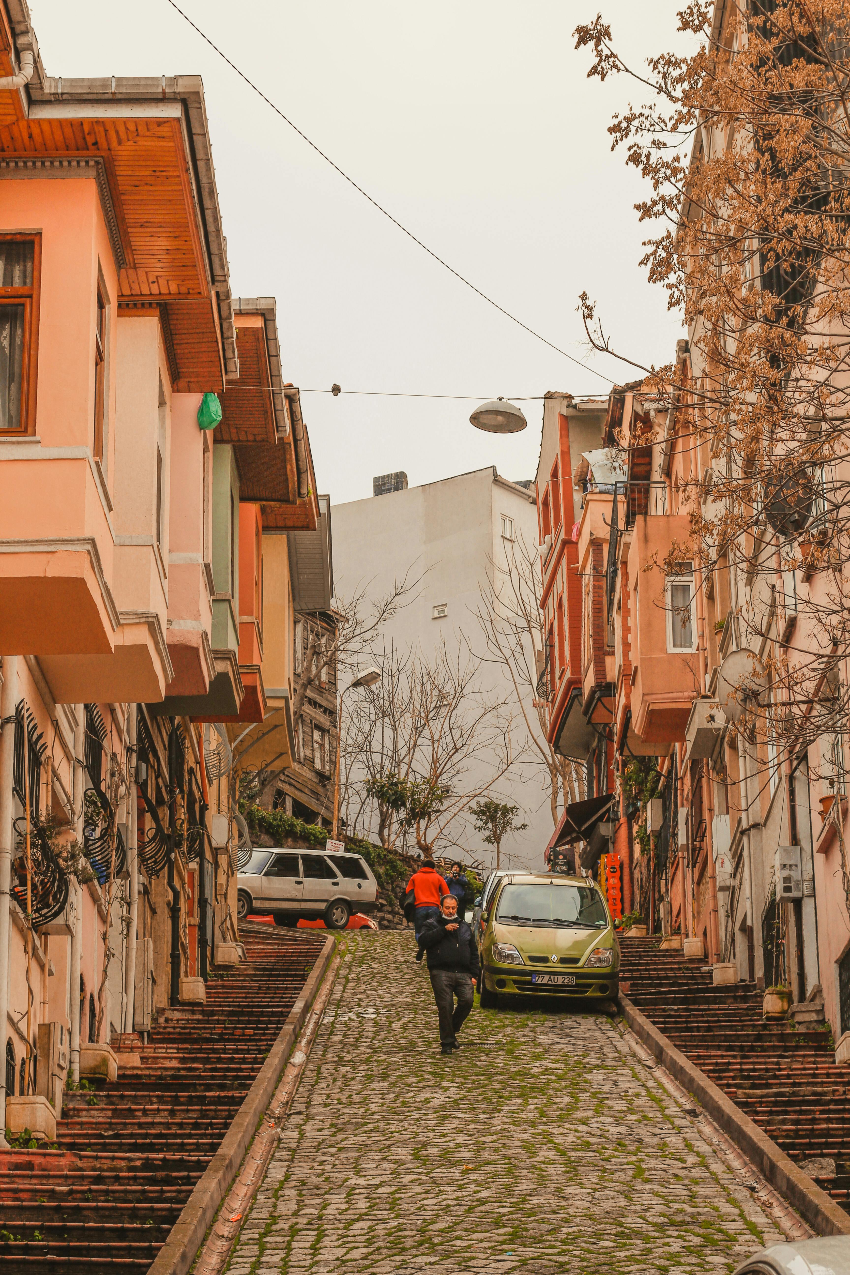 A Man Walking Down a Slanting Road with Parked Cars · Free Stock Photo