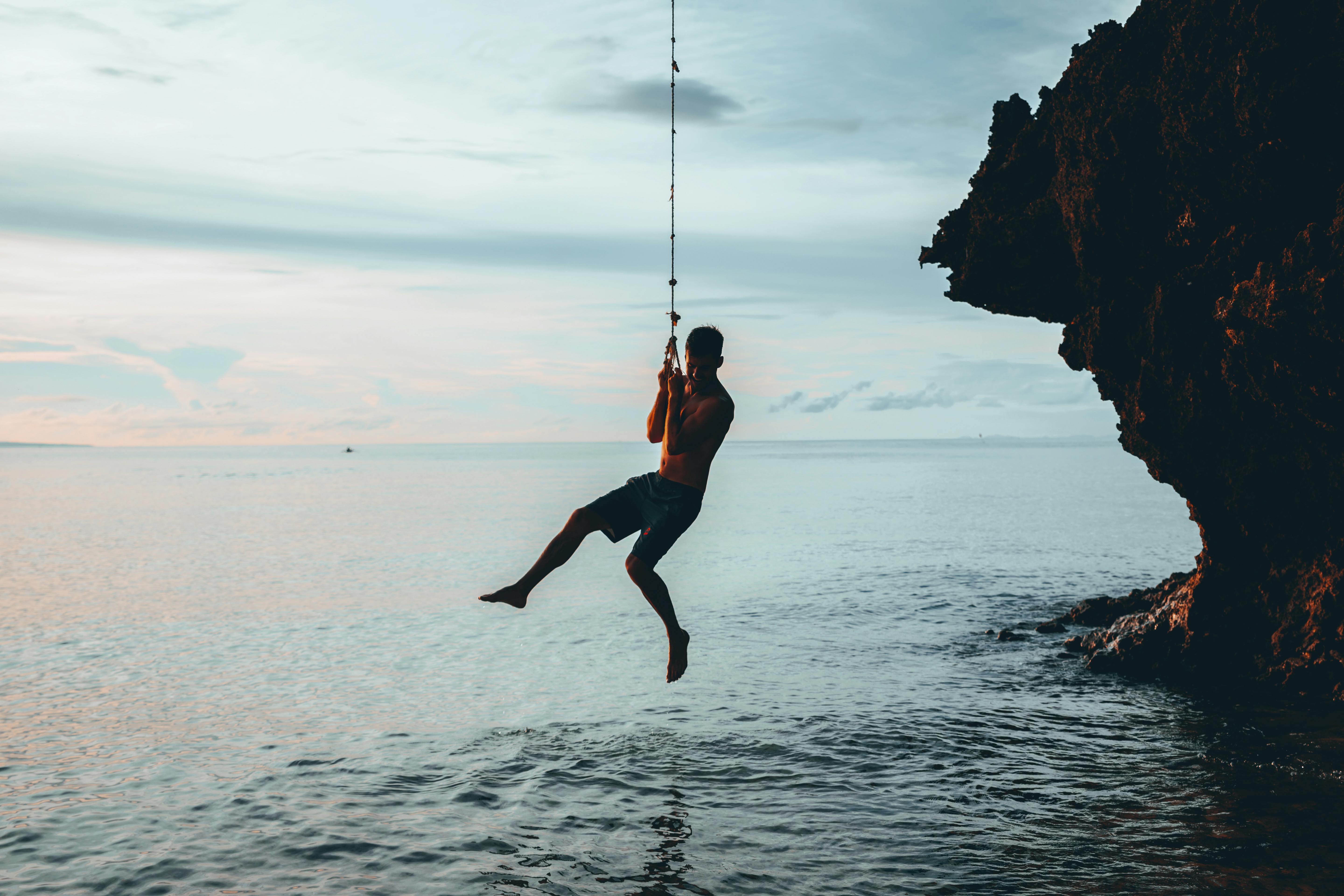 Man swinging on rope over sea · Free Stock Photo