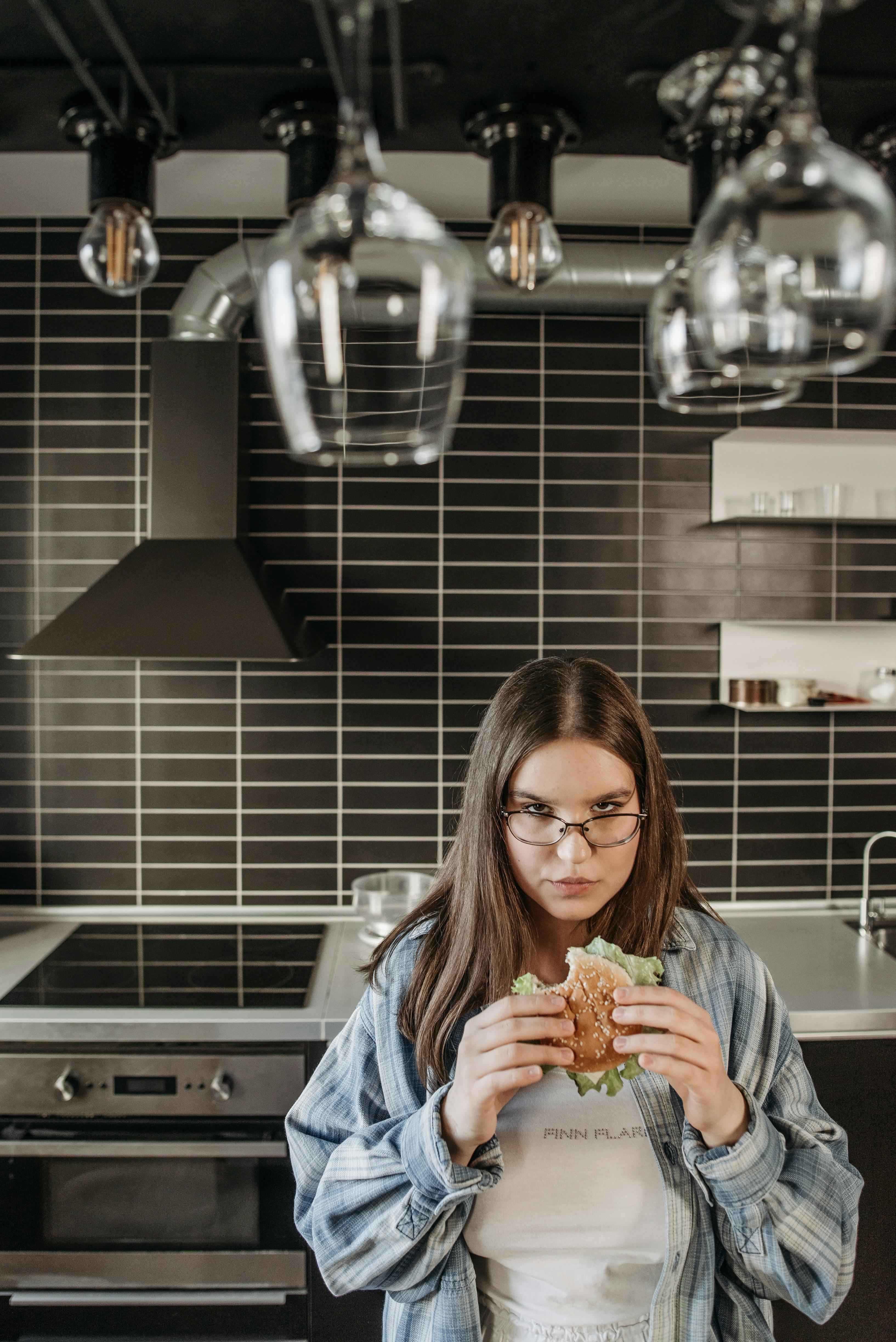 Woman Standing In The Kitchen Eating A Delicious Sandwich · Free Stock ...