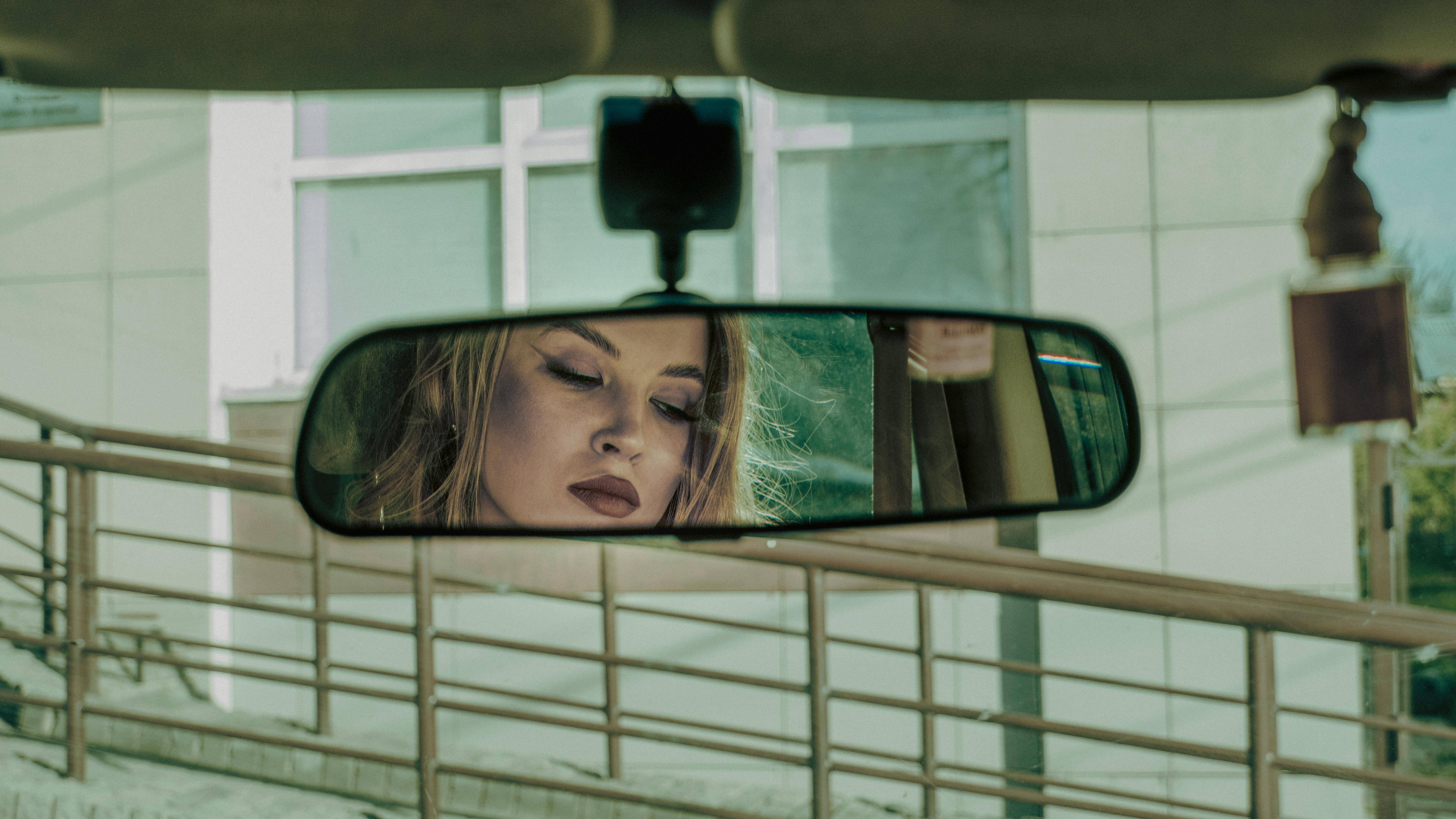 Lady reflecting in rearview mirror of automobile parked near building ...