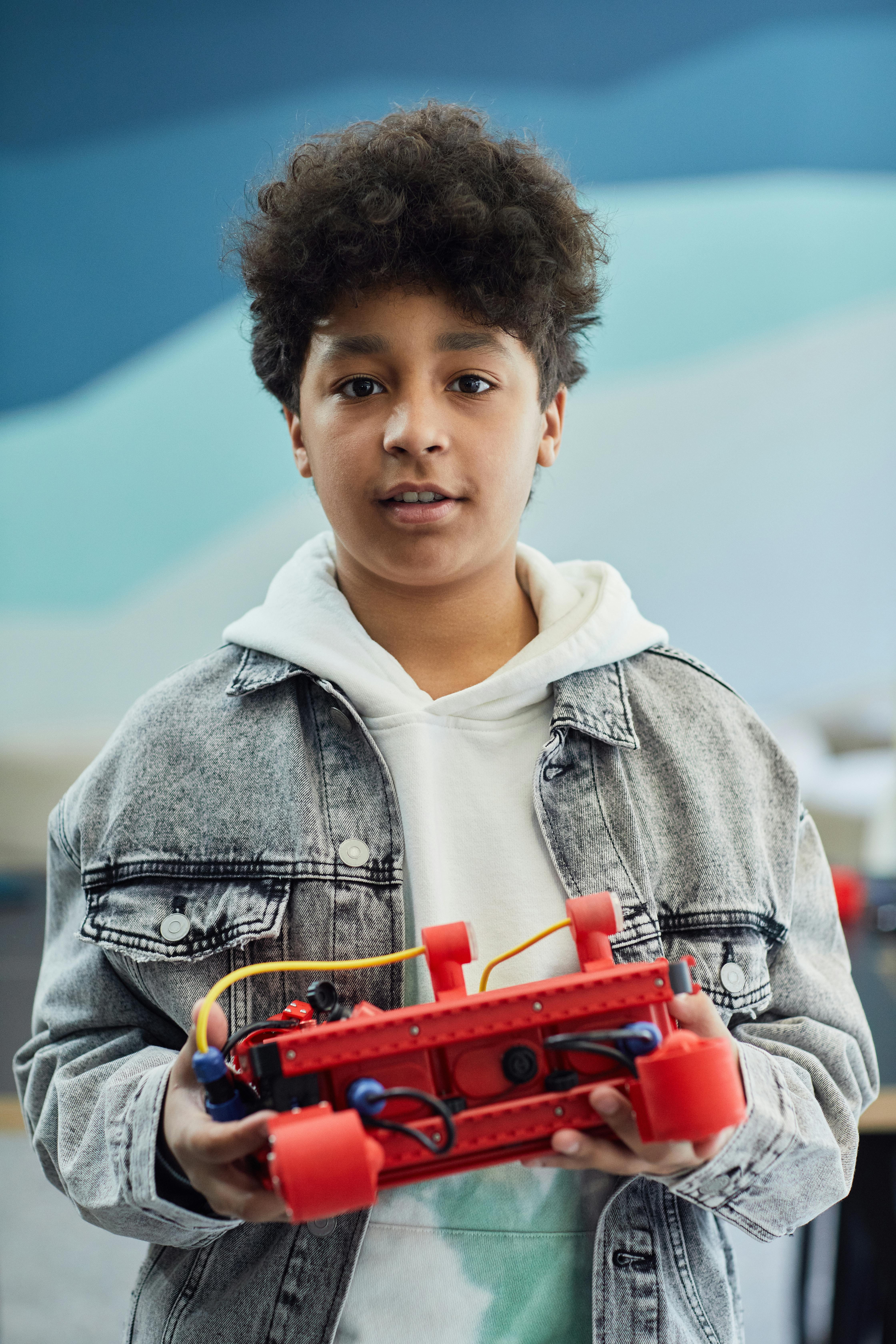 A Boy with Curly Hair Holding a Battery Operated Toy while Looking at ...