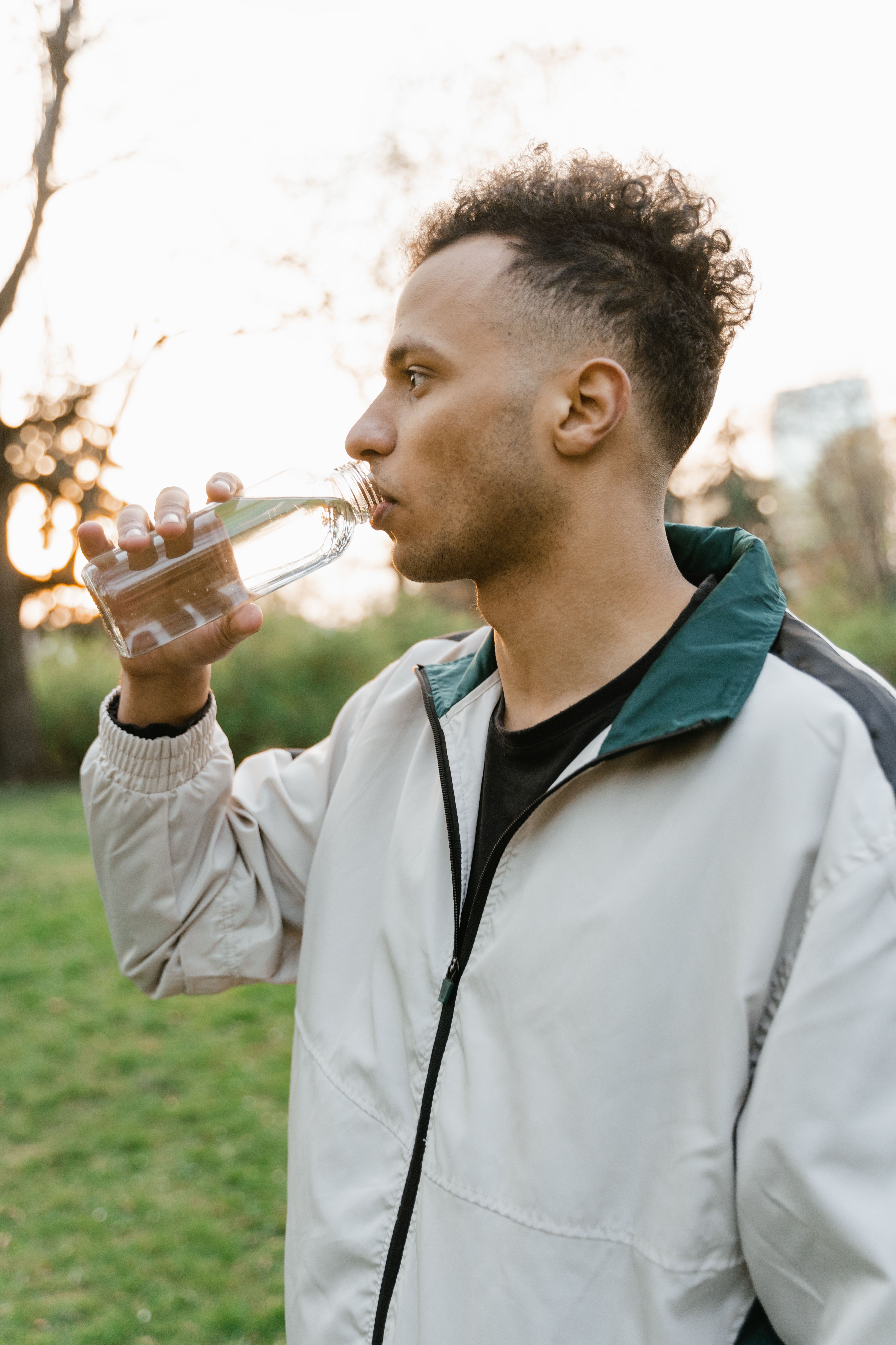 A Man Wearing White and Green Jacket Drinking Water from a Clear Bottle ...