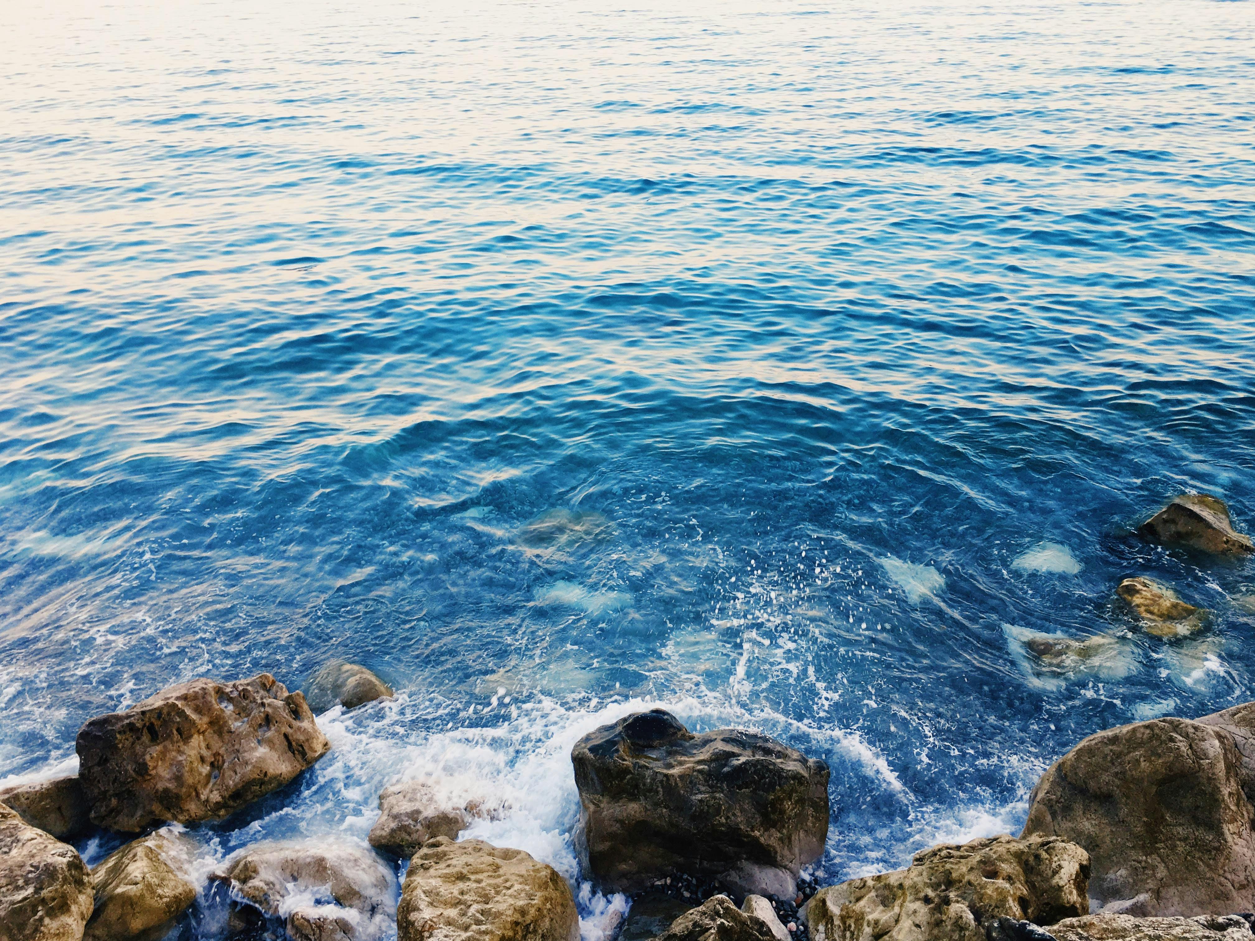 Turquoise sea water washing coast with stones · Free Stock Photo